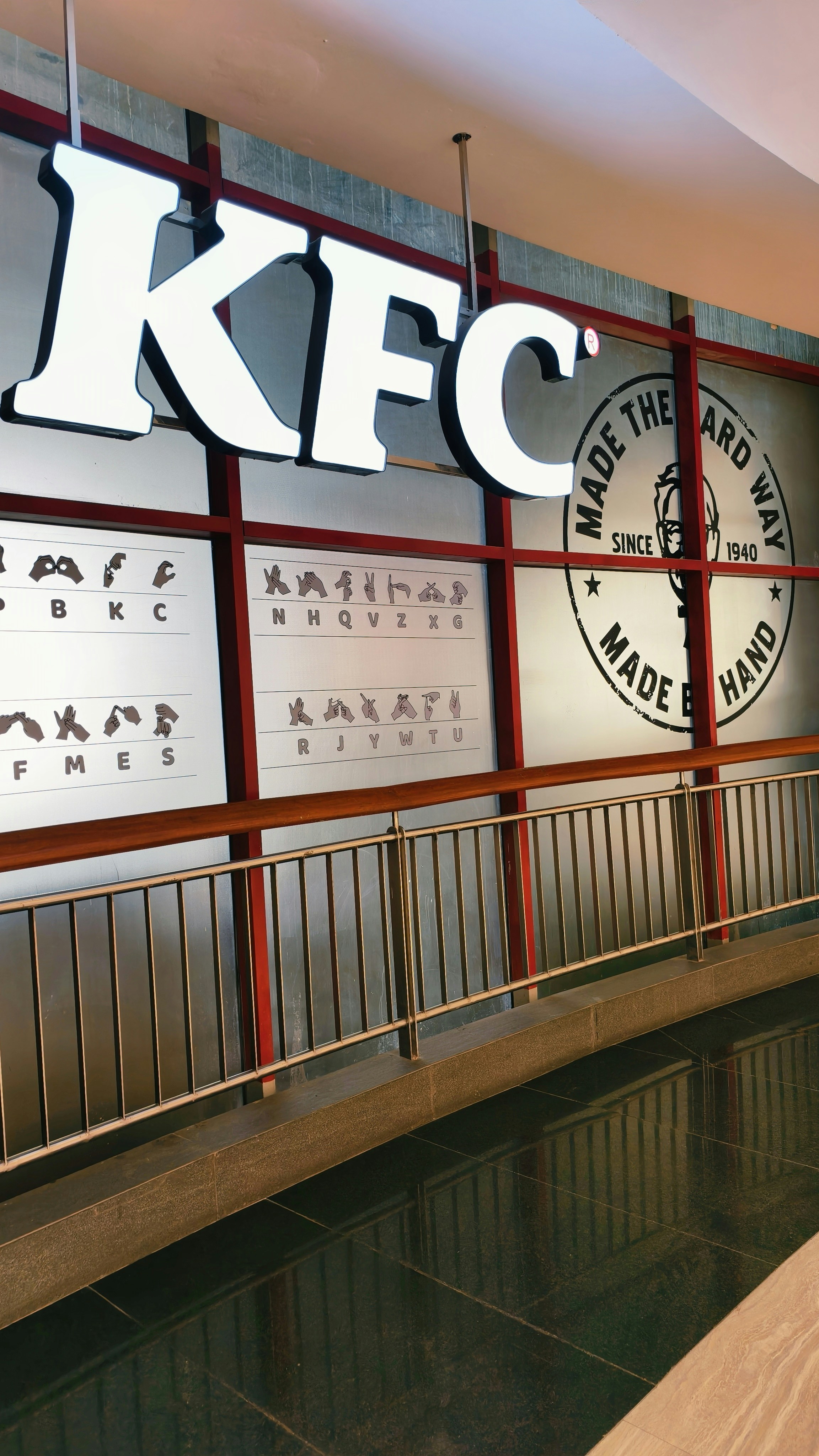 A KFC sign above a glass wall with sign language alphabet illustrations
