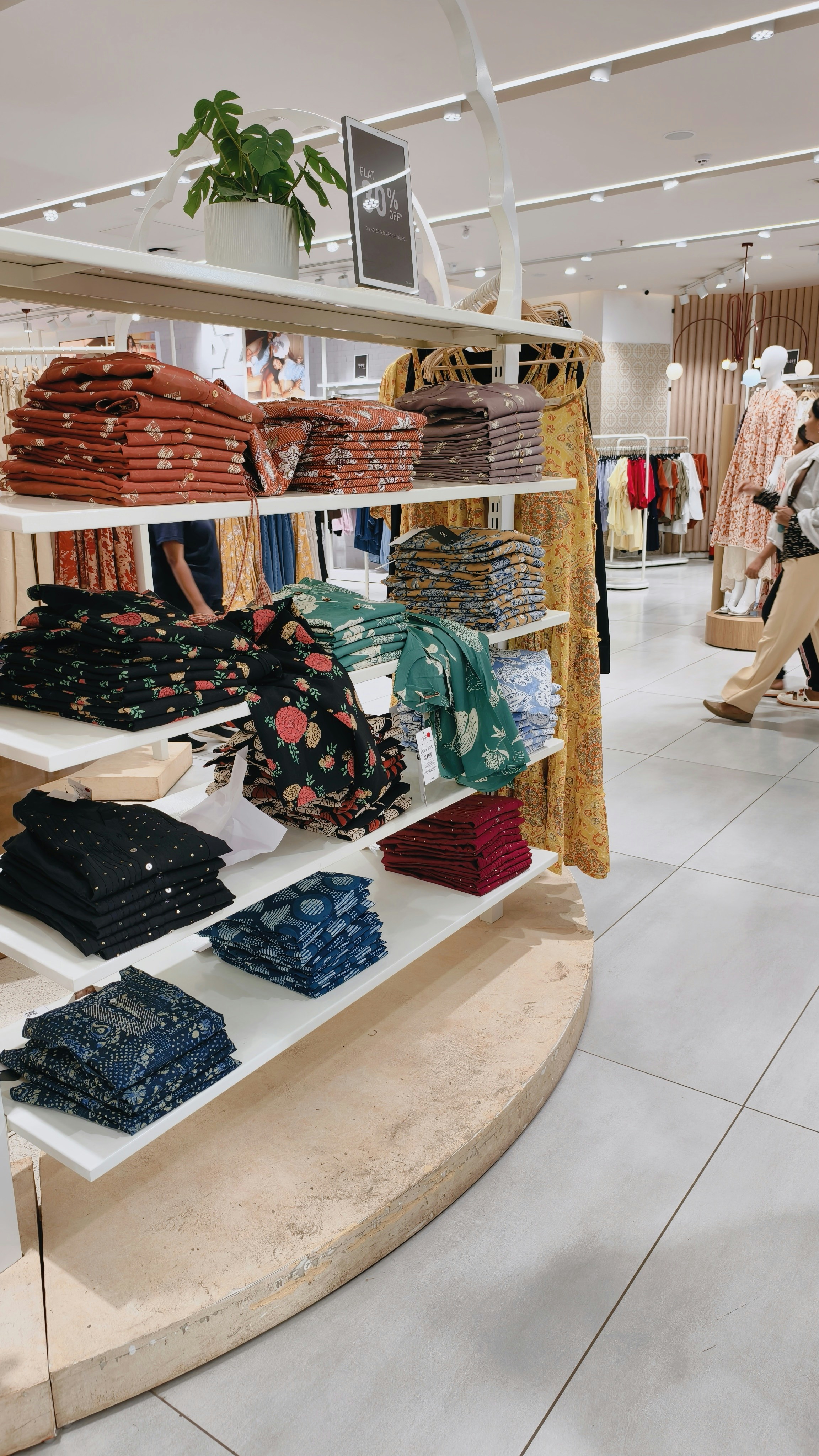 Colorful folded fabrics and garments arranged on a curved display shelf in a bright retail space.