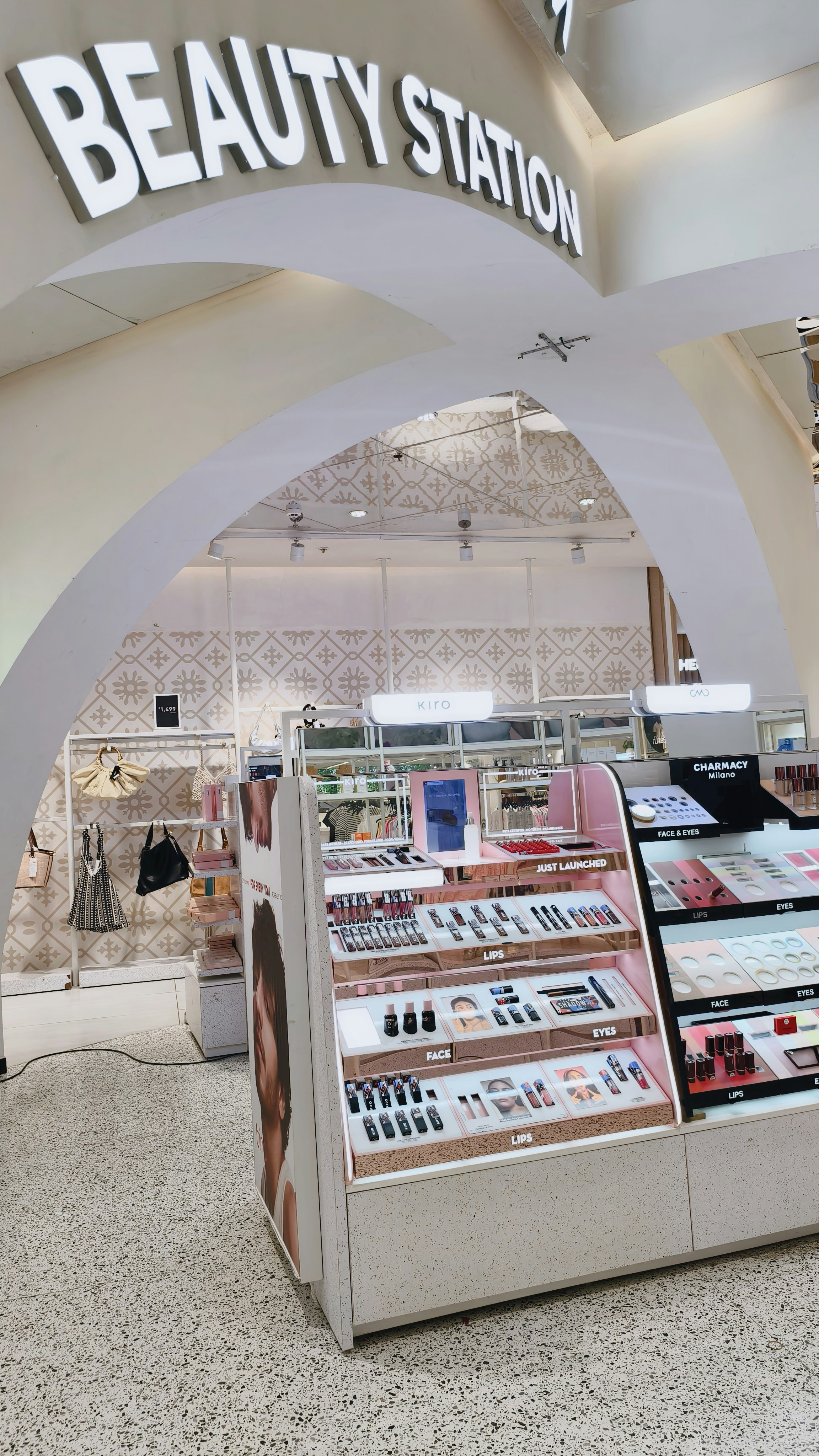 Display of cosmetics on tiered shelves inside a beauty store under a curved arch and prominent signage. A bright, softly lit interior with organized product rows and labeled sections.