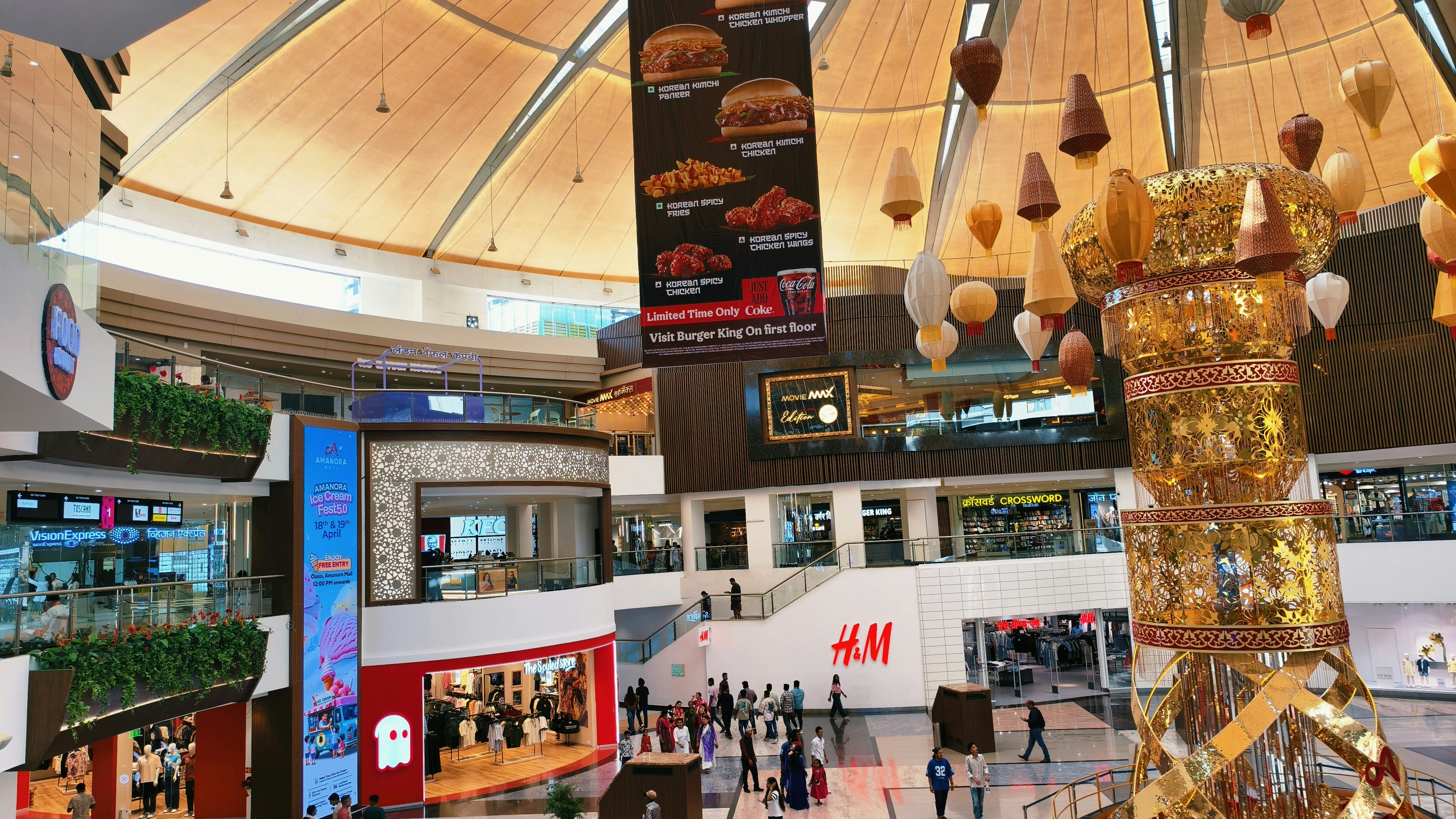 Lively shopping mall interior with a tall decorative sculpture and storefronts across multiple levels.
