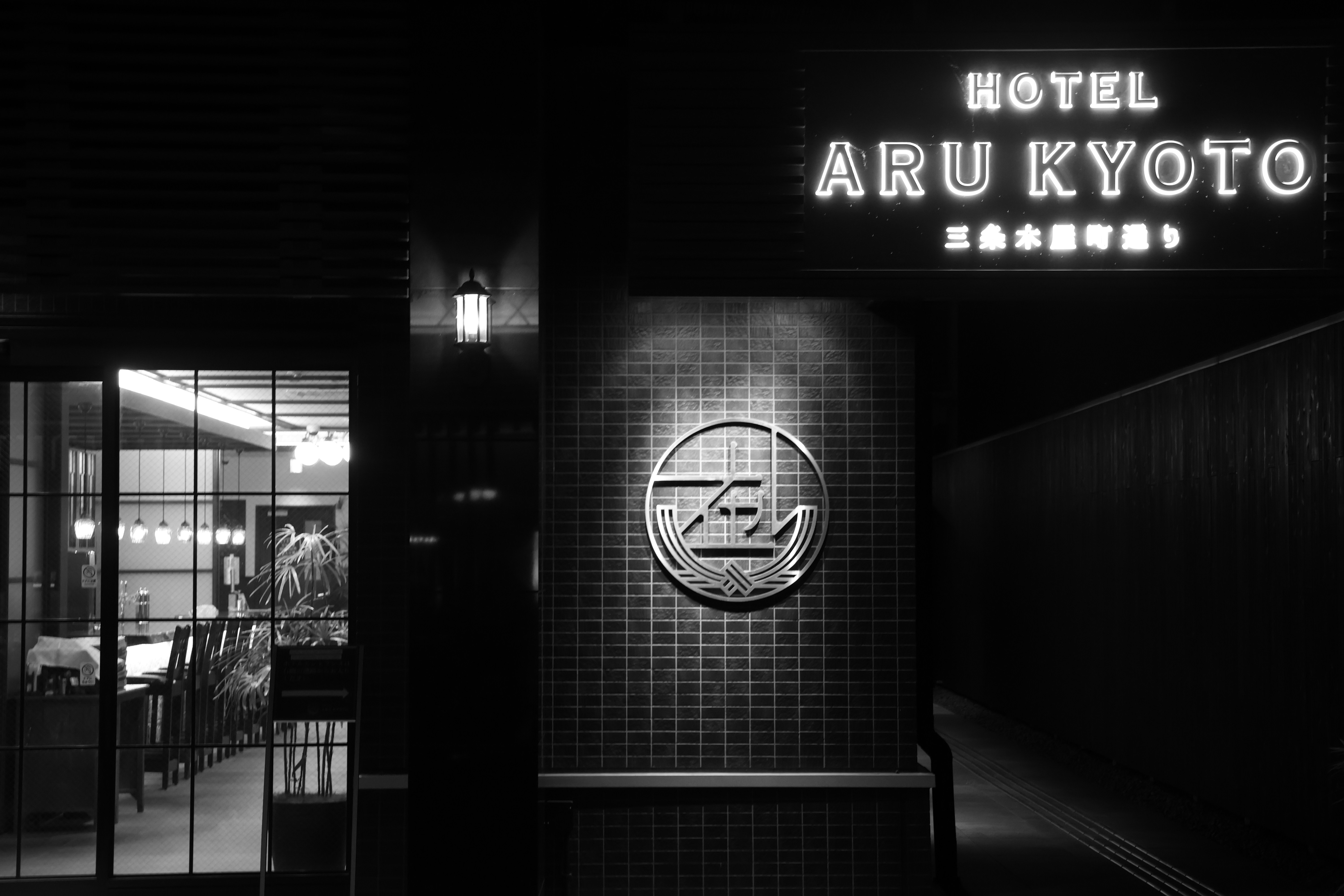 A glowing sign reading HOTEL ARU KYOTO above a tiled wall at night