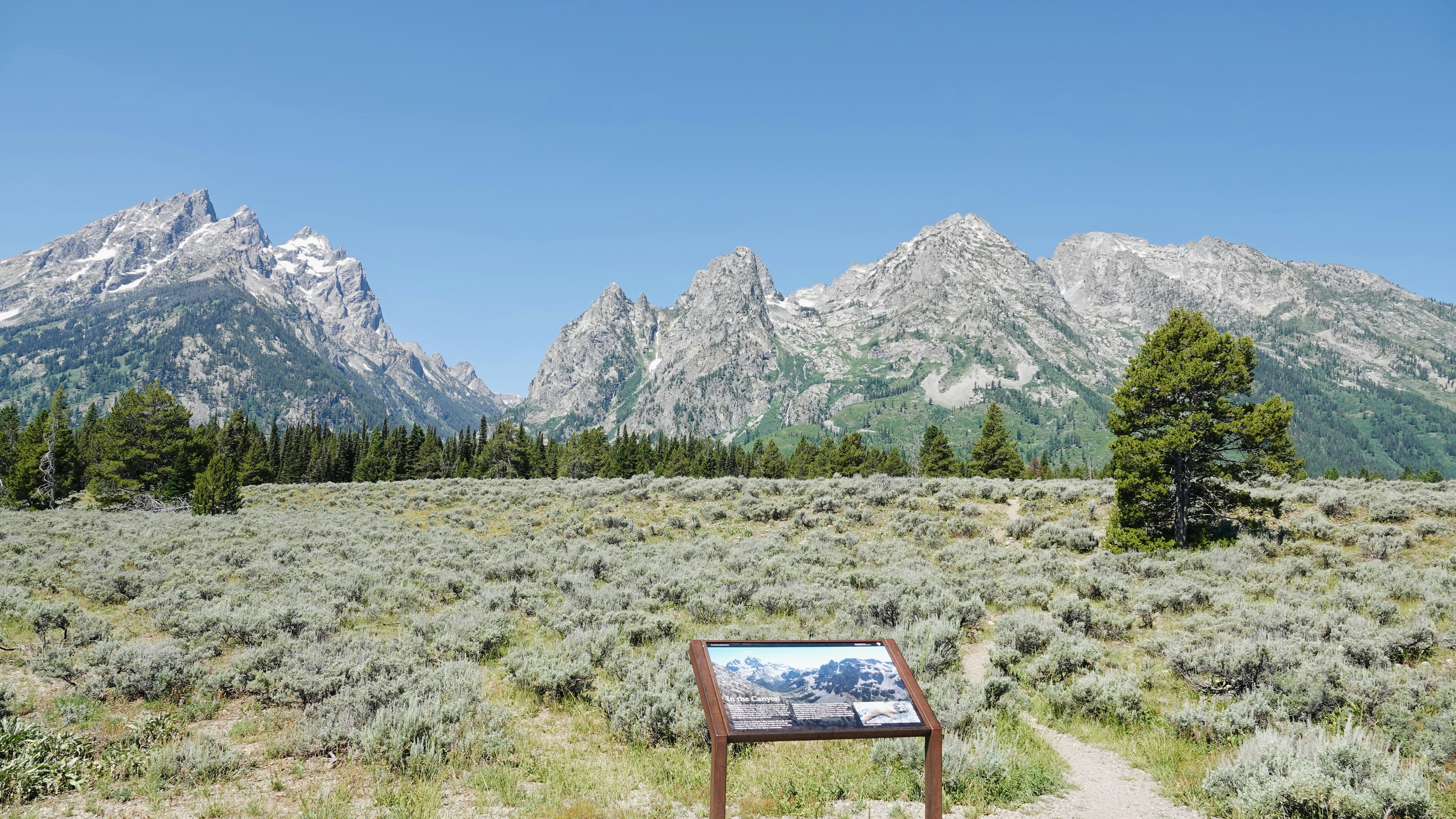 Trail marker and alpine backdrop under a blue sky