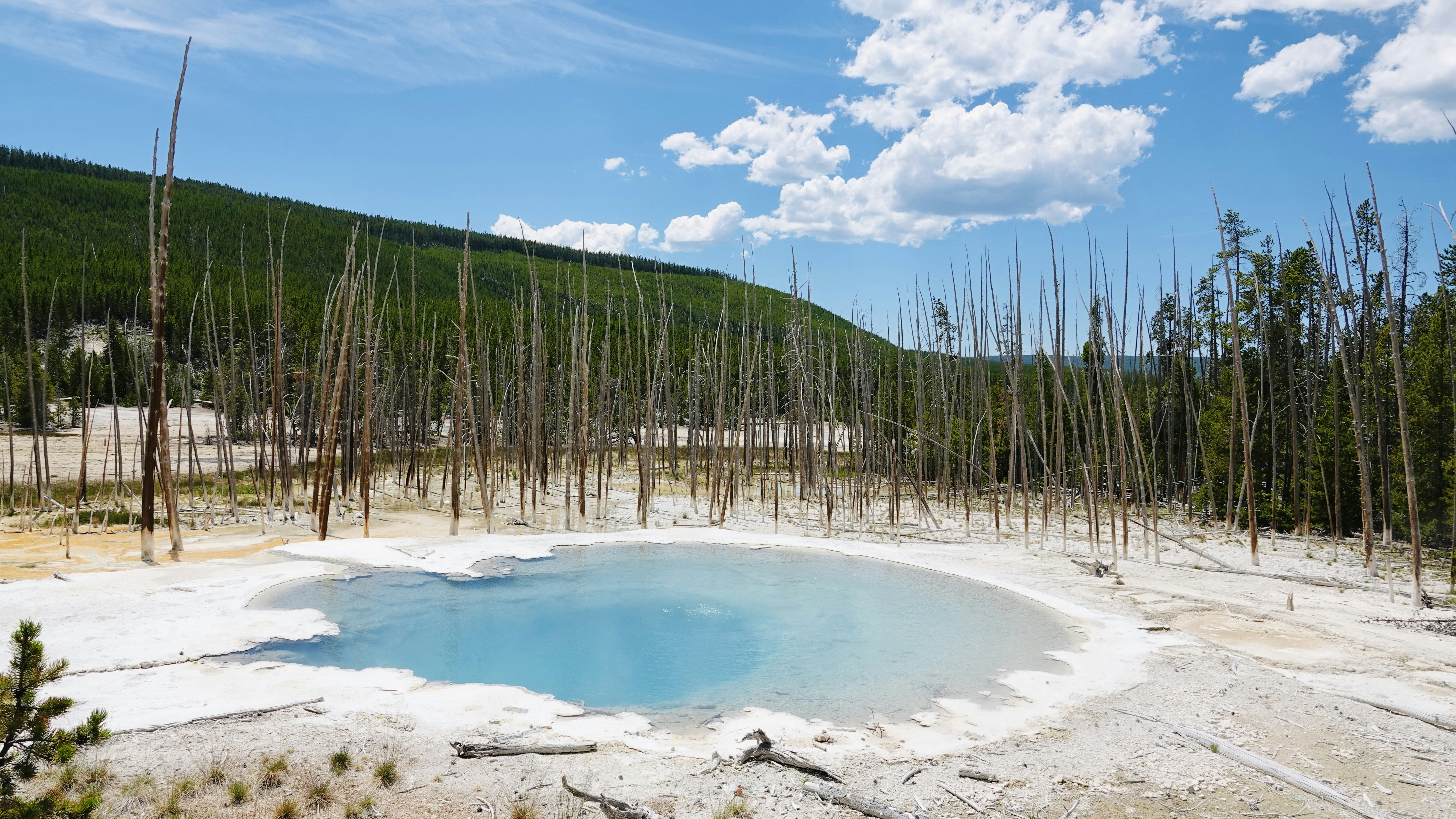 Blue crater pool amid ghostly white terraces under a bright alpine sky