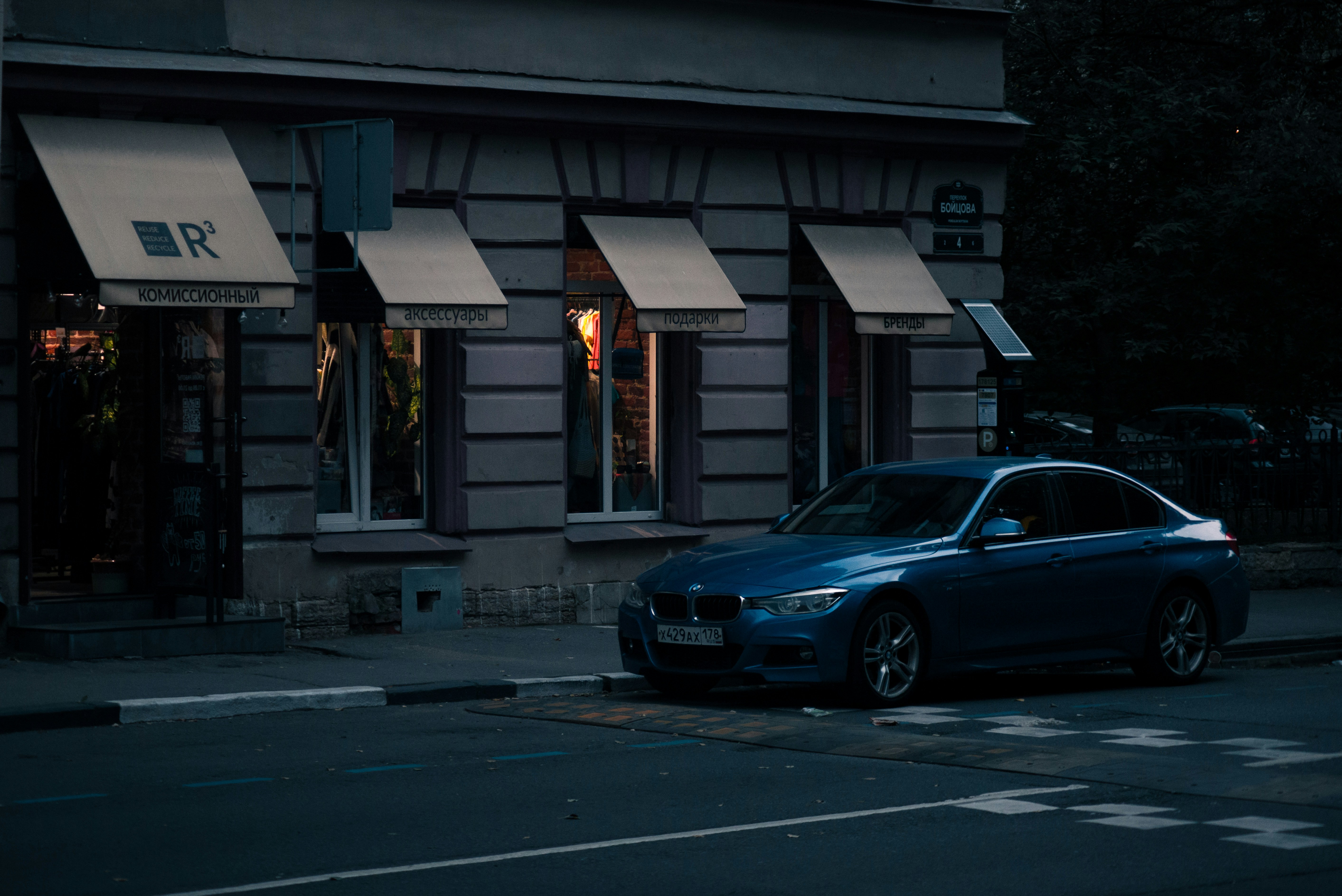 Blue sedan under streetlights: quiet storefront dusk