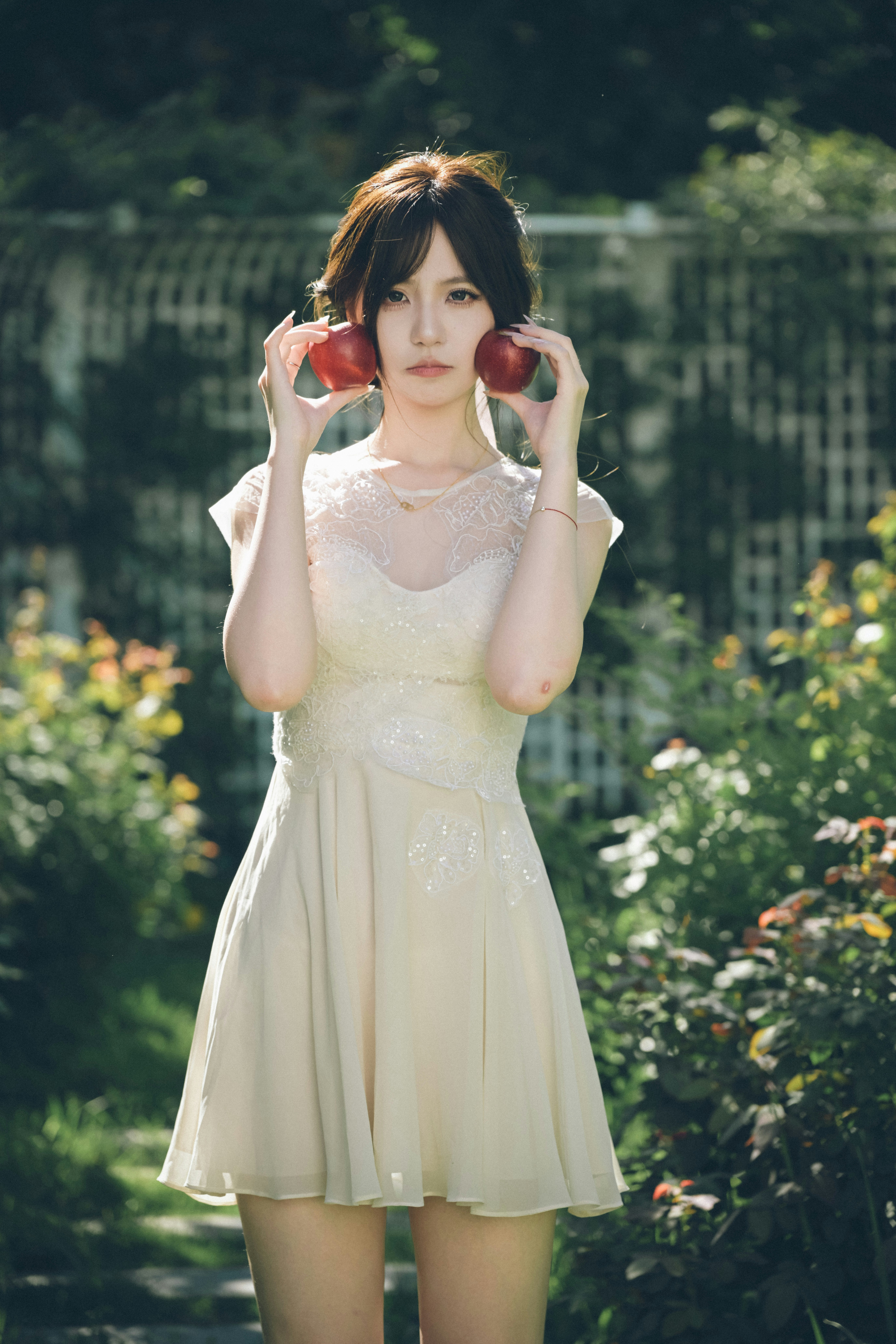 Portrait in Soft Sunlight: A Woman with Red Apples by a Garden Fence