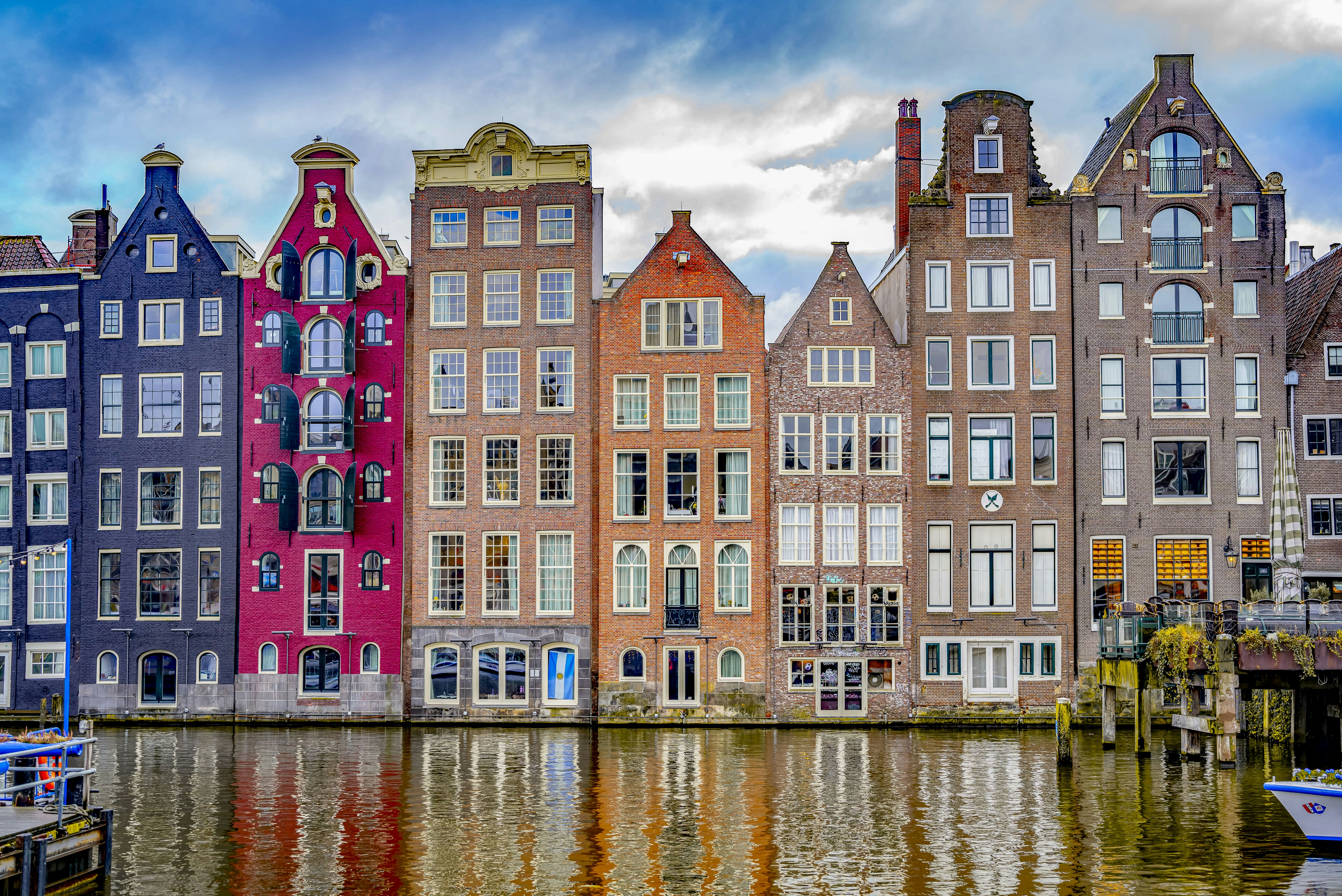 Row of tall, colorful canal houses reflected in still water along a European harbor.