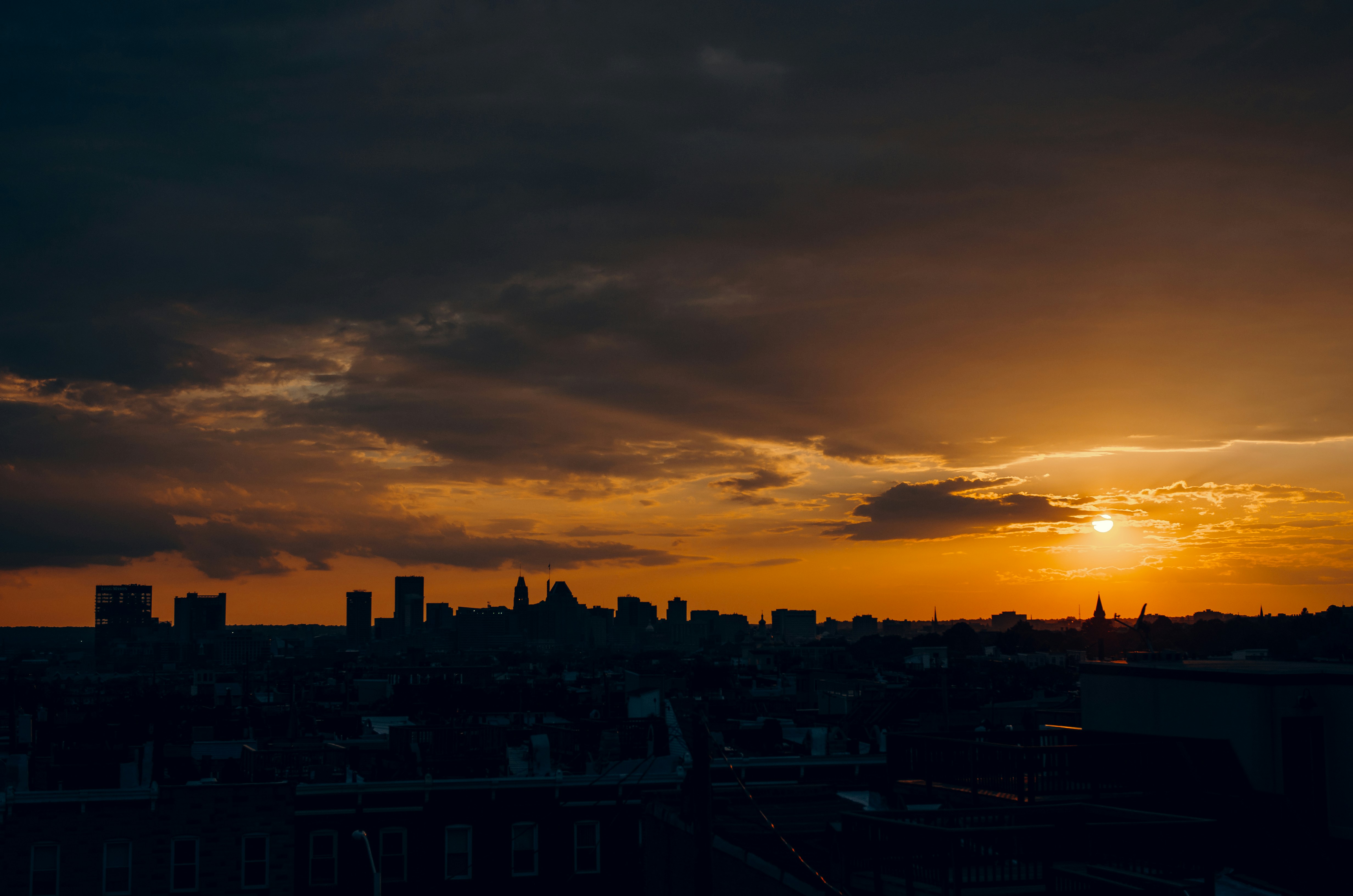 Dusk settles over a low city skyline as warm orange light washes the horizon and silhouettes the buildings.