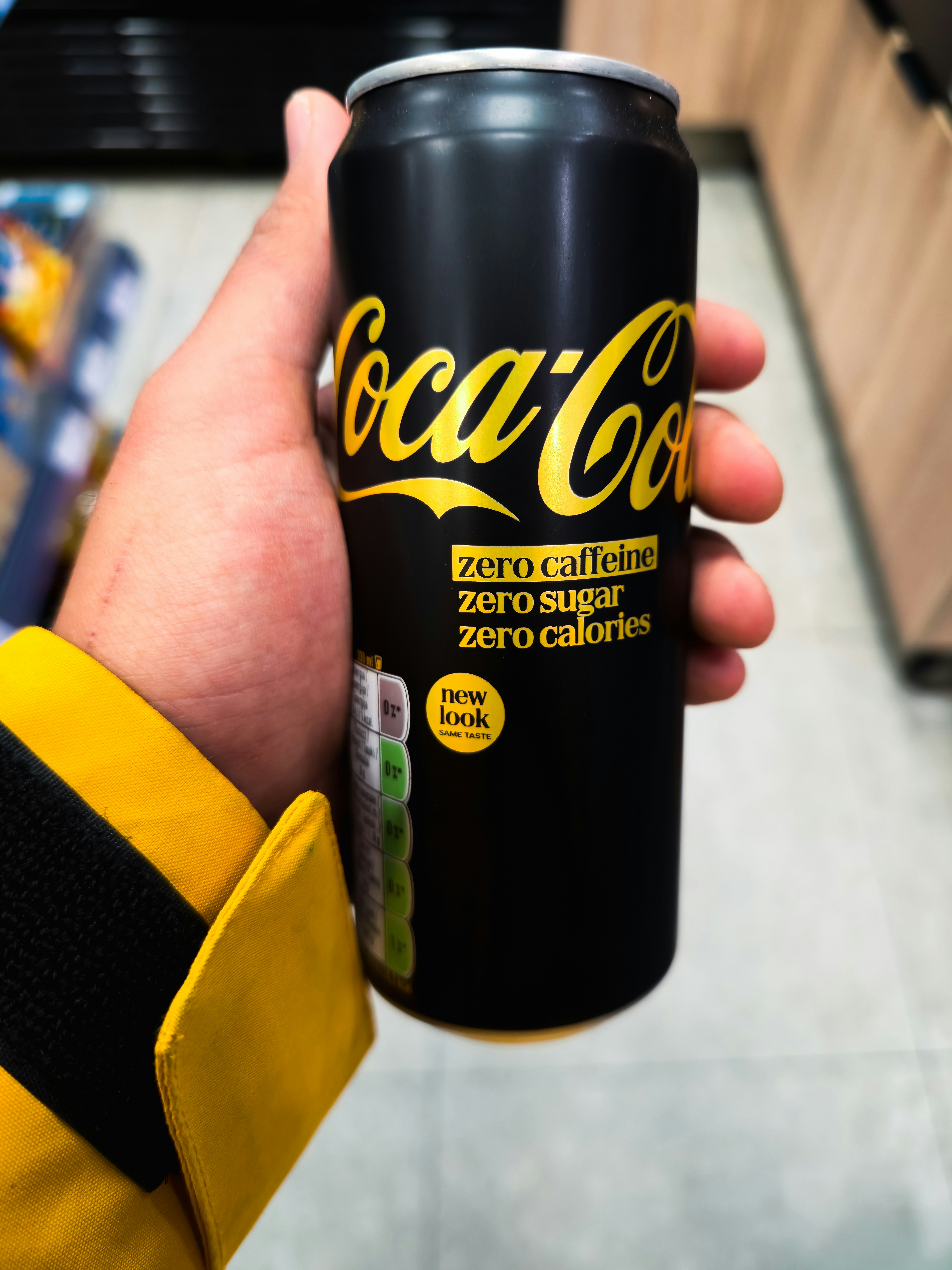 Coca-Cola Zero Caffeine Grip: A hand-cradled can in a bright supermarket aisle