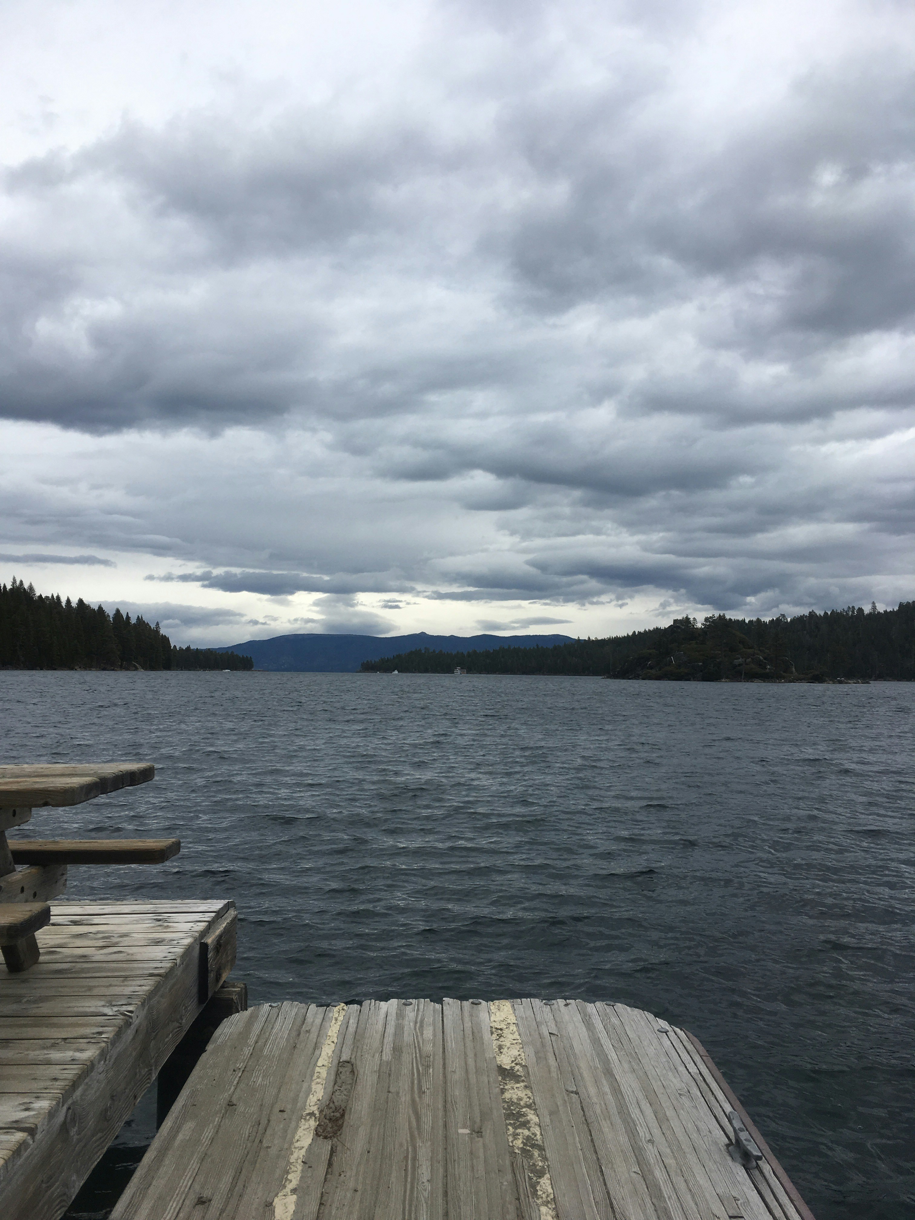 Calm lake extends to distant shoreline under overcast skies; wooden dock boards lead the eye toward the horizon.