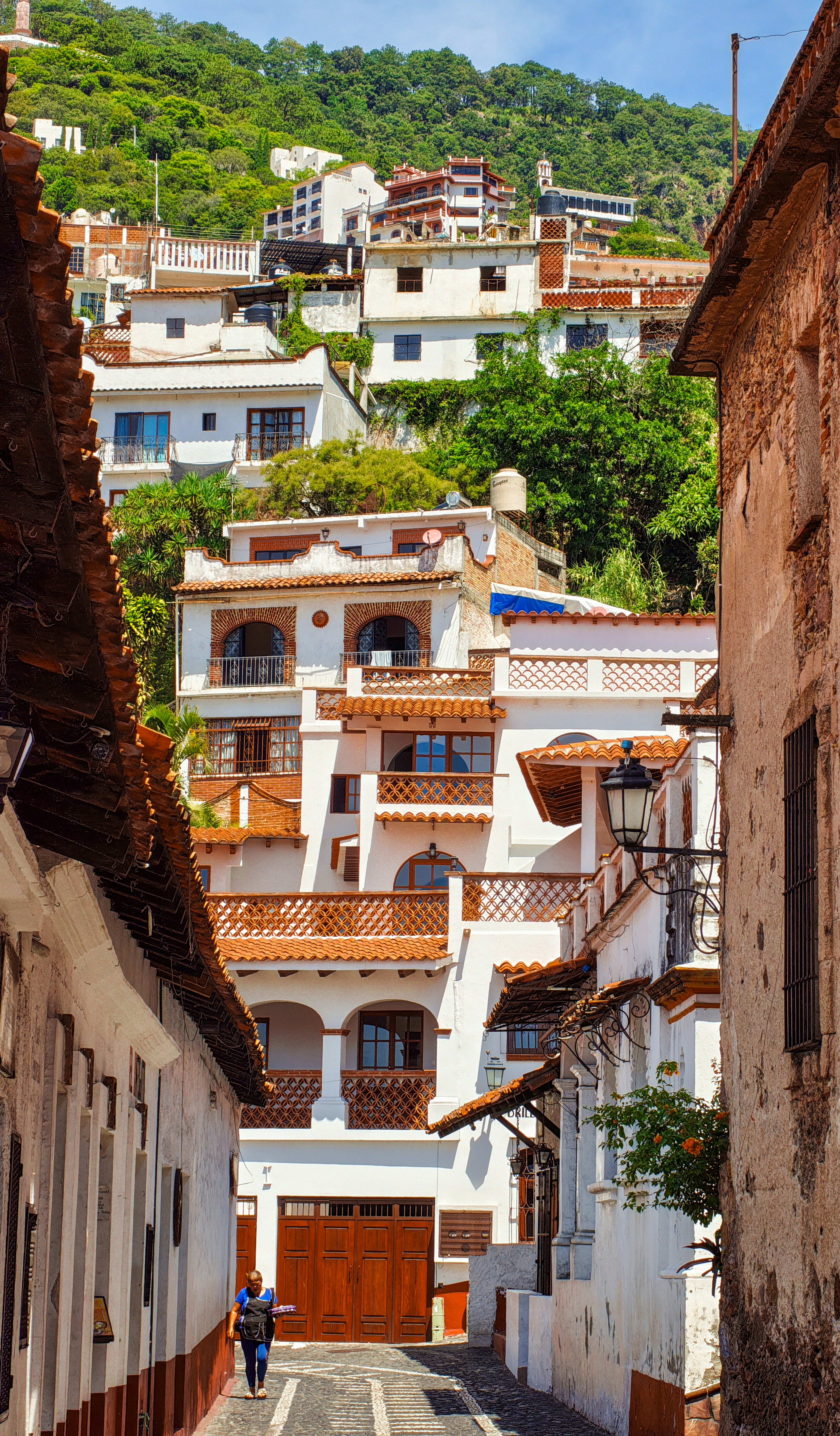 A person walking down a narrow cobblestone street lined with white buildings in Taxco