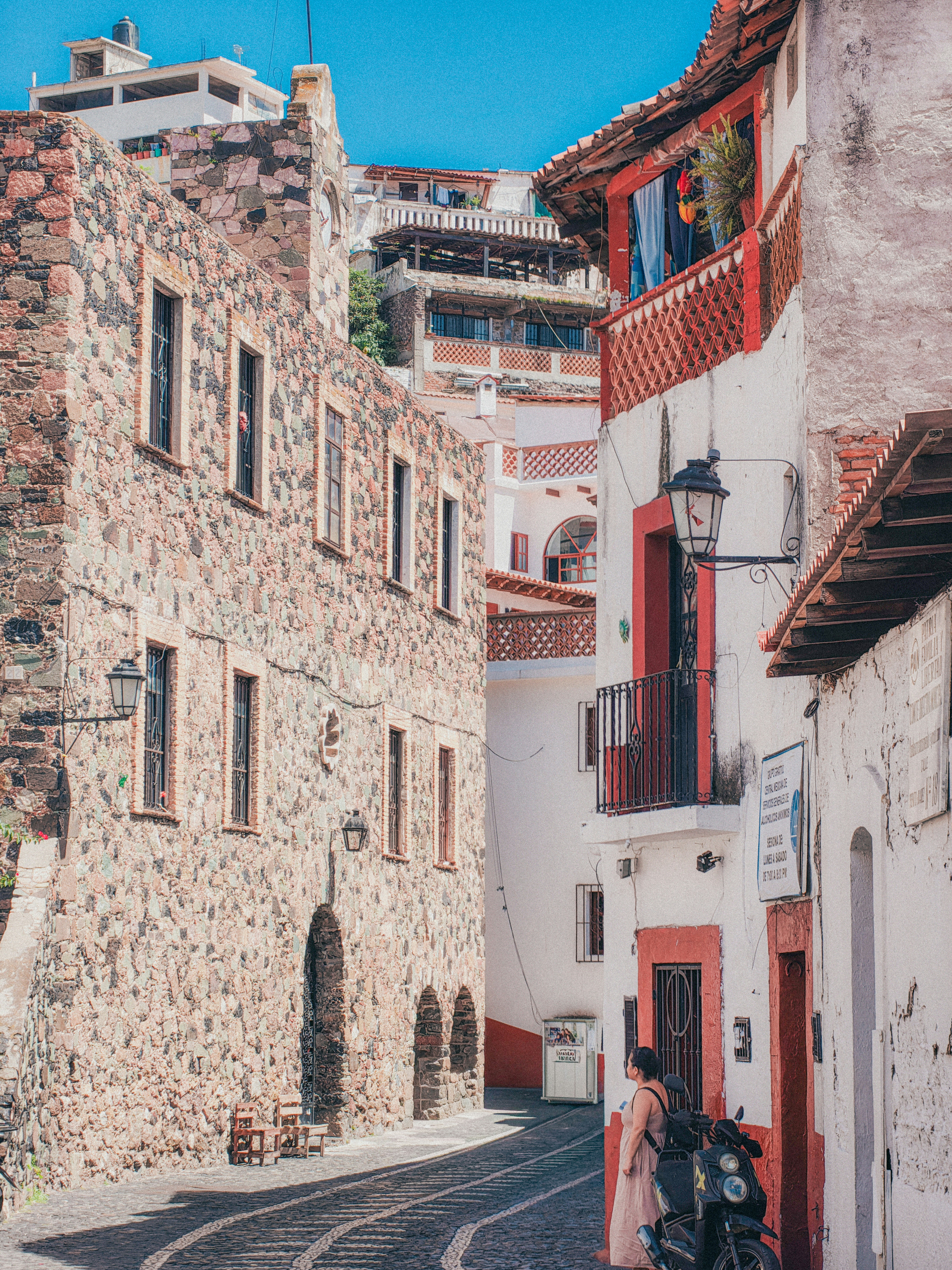 A person standing by a scooter on a narrow cobblestone street in Taxco