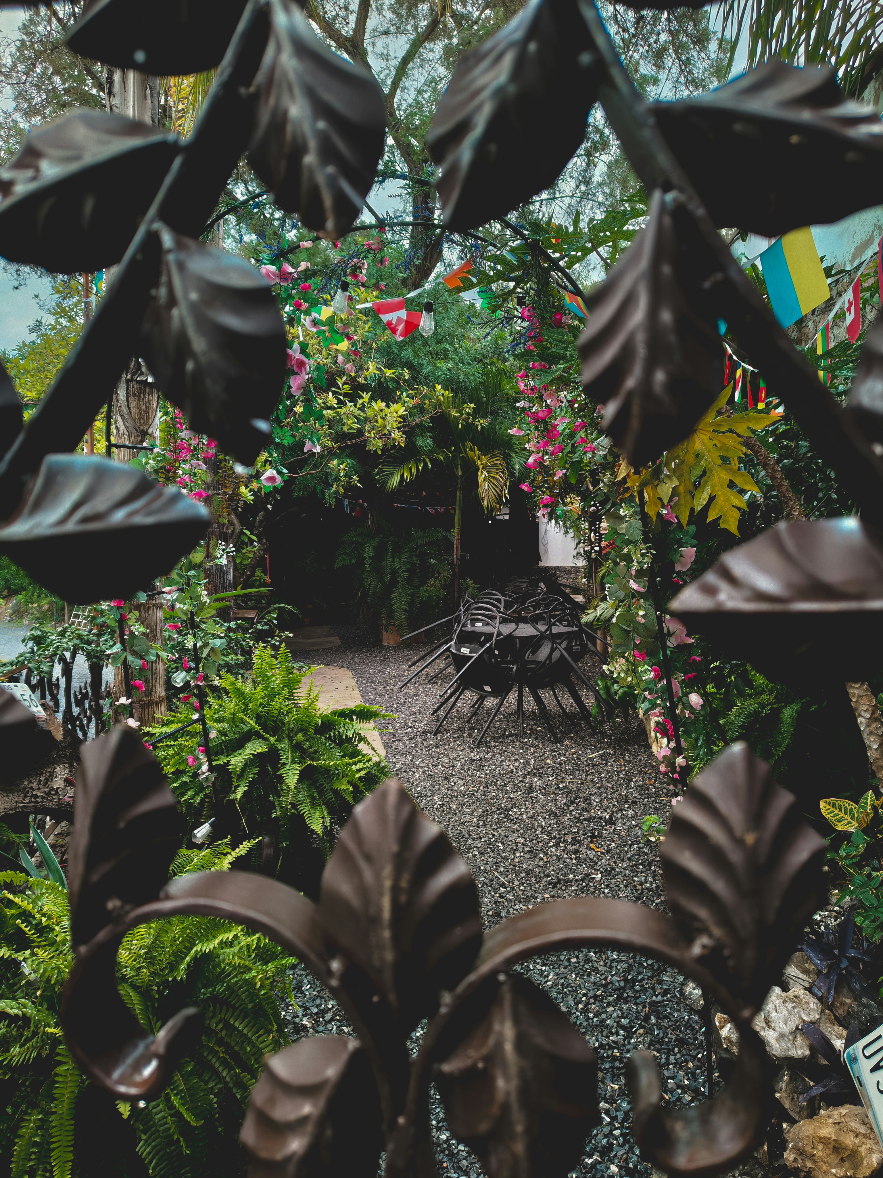 A gravel patio with stacked chairs framed by a decorative metal gate and flowers