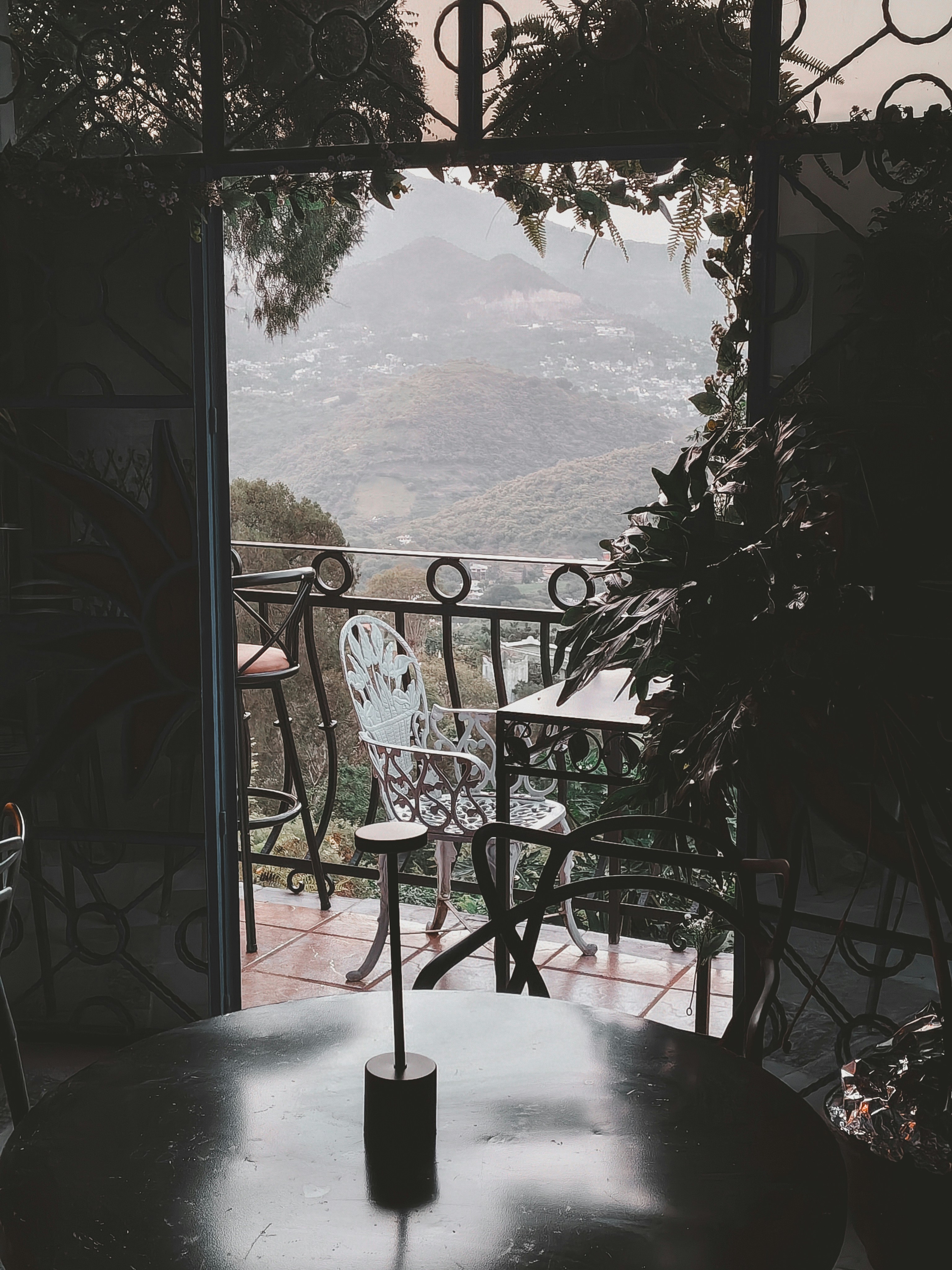 A balcony with metal chairs overlooking a hazy mountain landscape at dusk