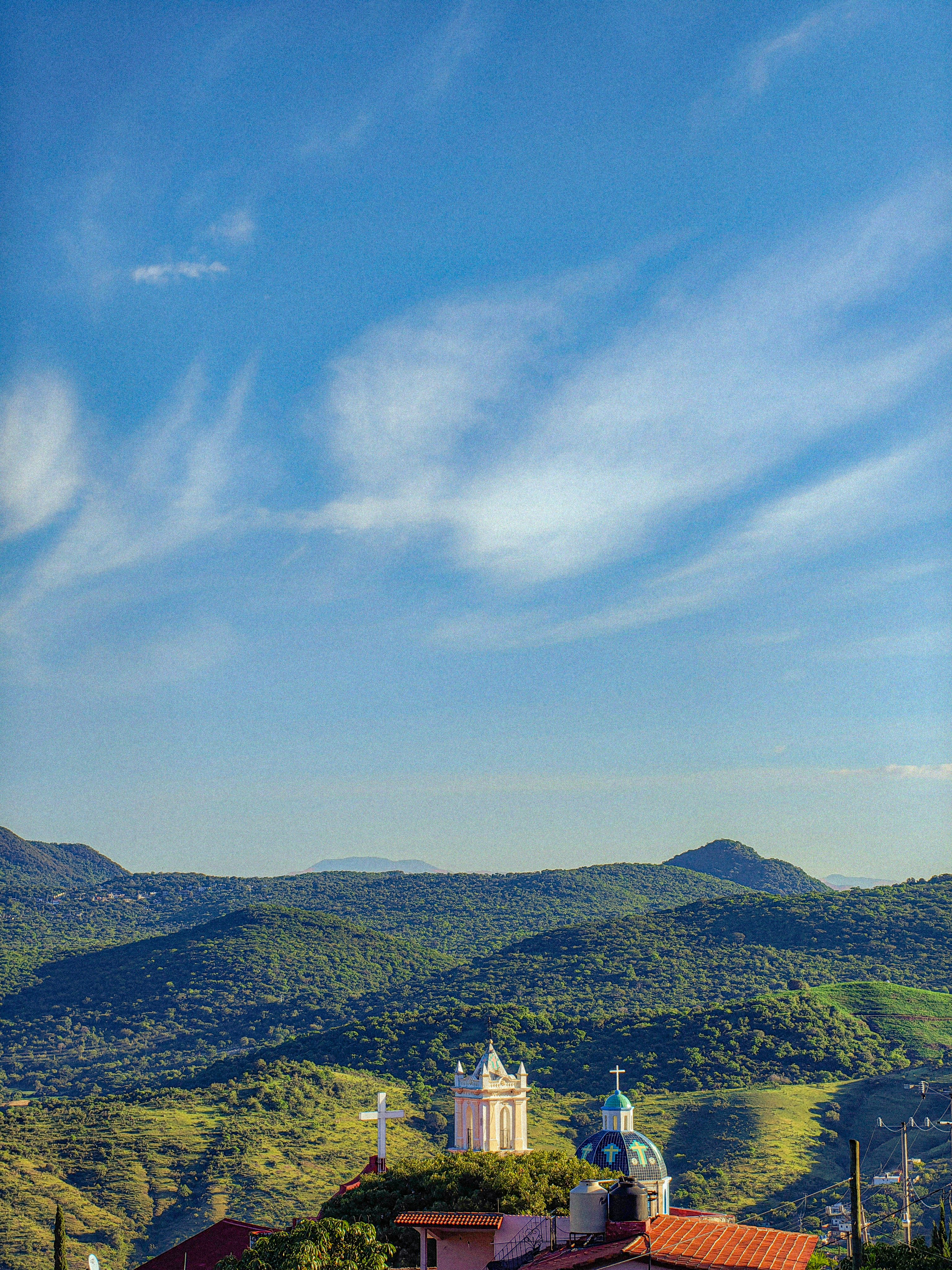 A church tower and blue dome among green hills under a bright sky