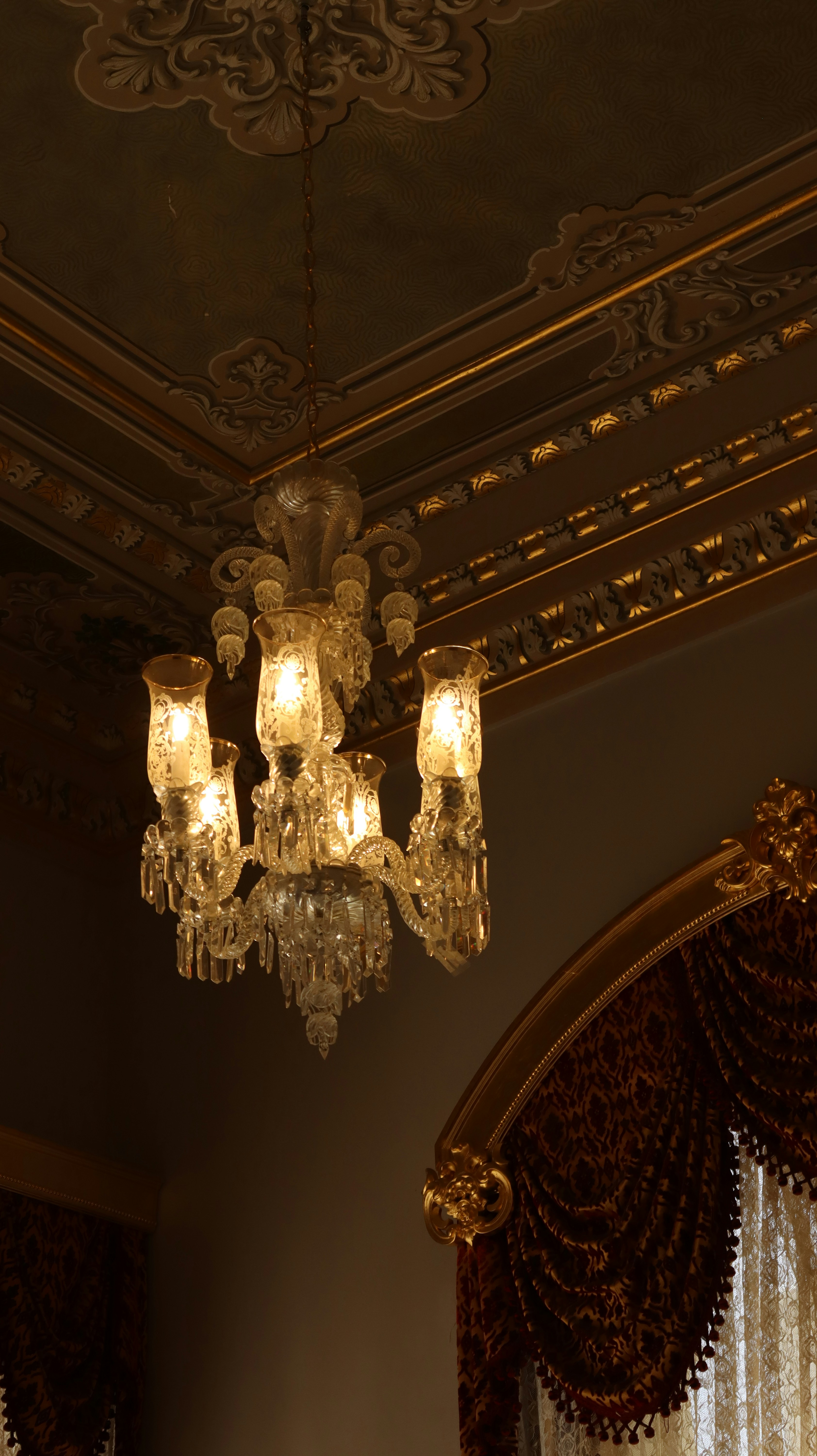 Crystal chandelier glow under ornate ceiling in velvet-draped interior
