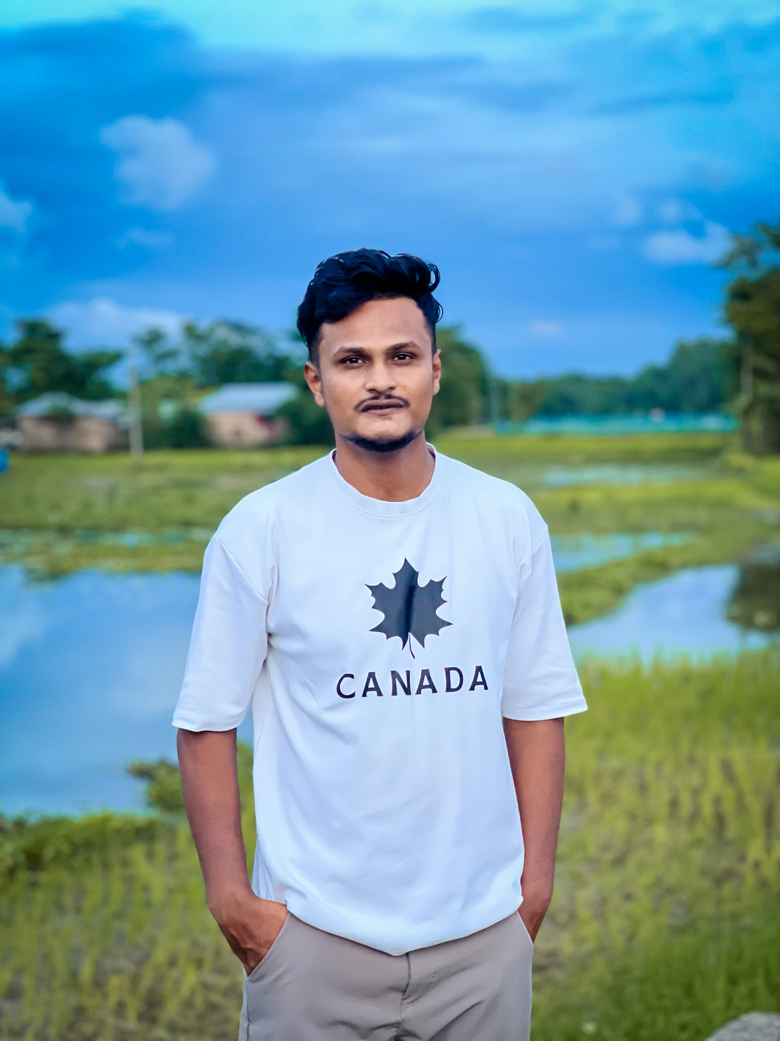 Portrait in a Quiet Orchard: A Young Man in a Canada T‑shirt Stands by Teal Waters