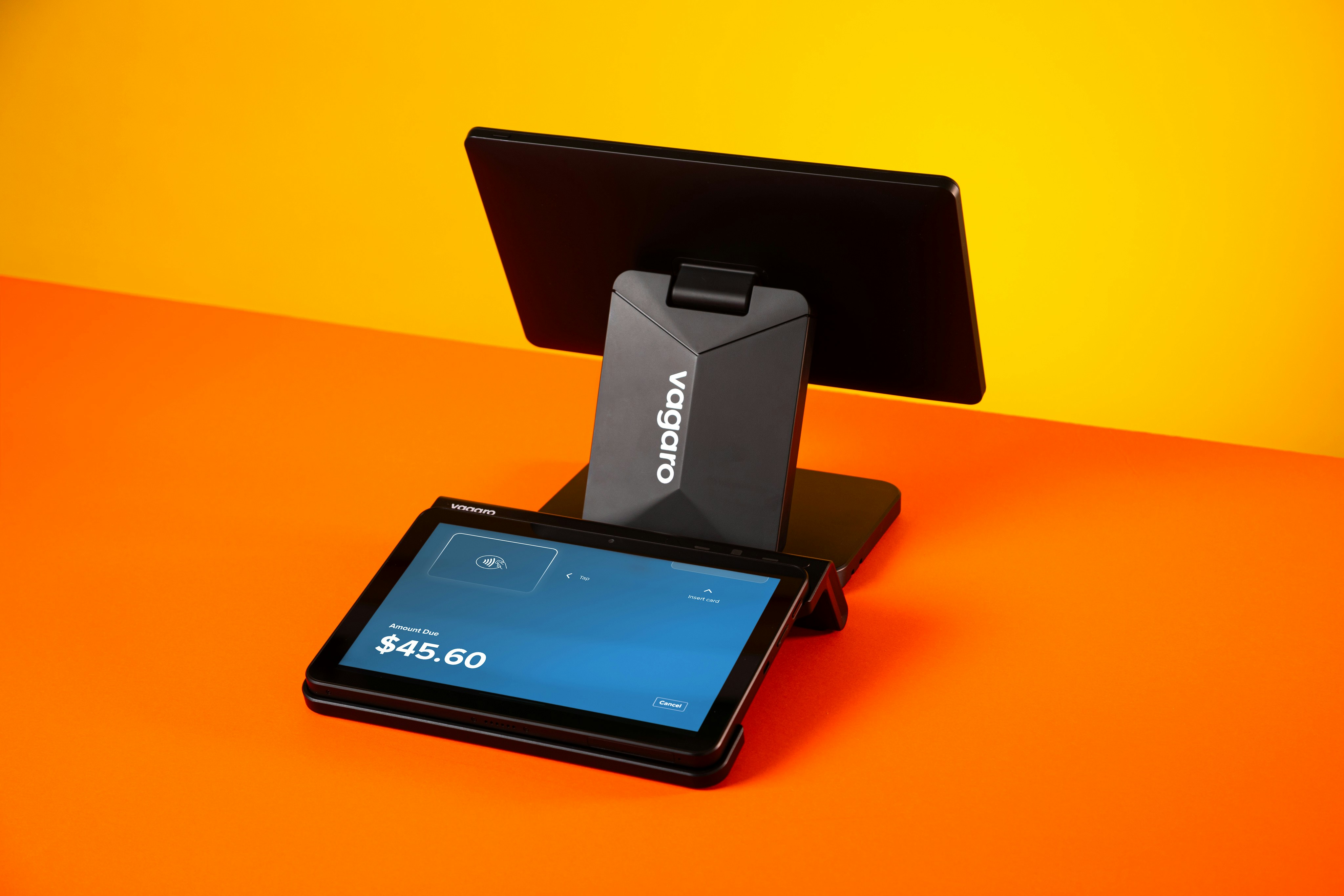 Compact payment device with a detachable screen sits on an orange surface against a yellow backdrop, highlighting its card-reading interface and modern stand design.
