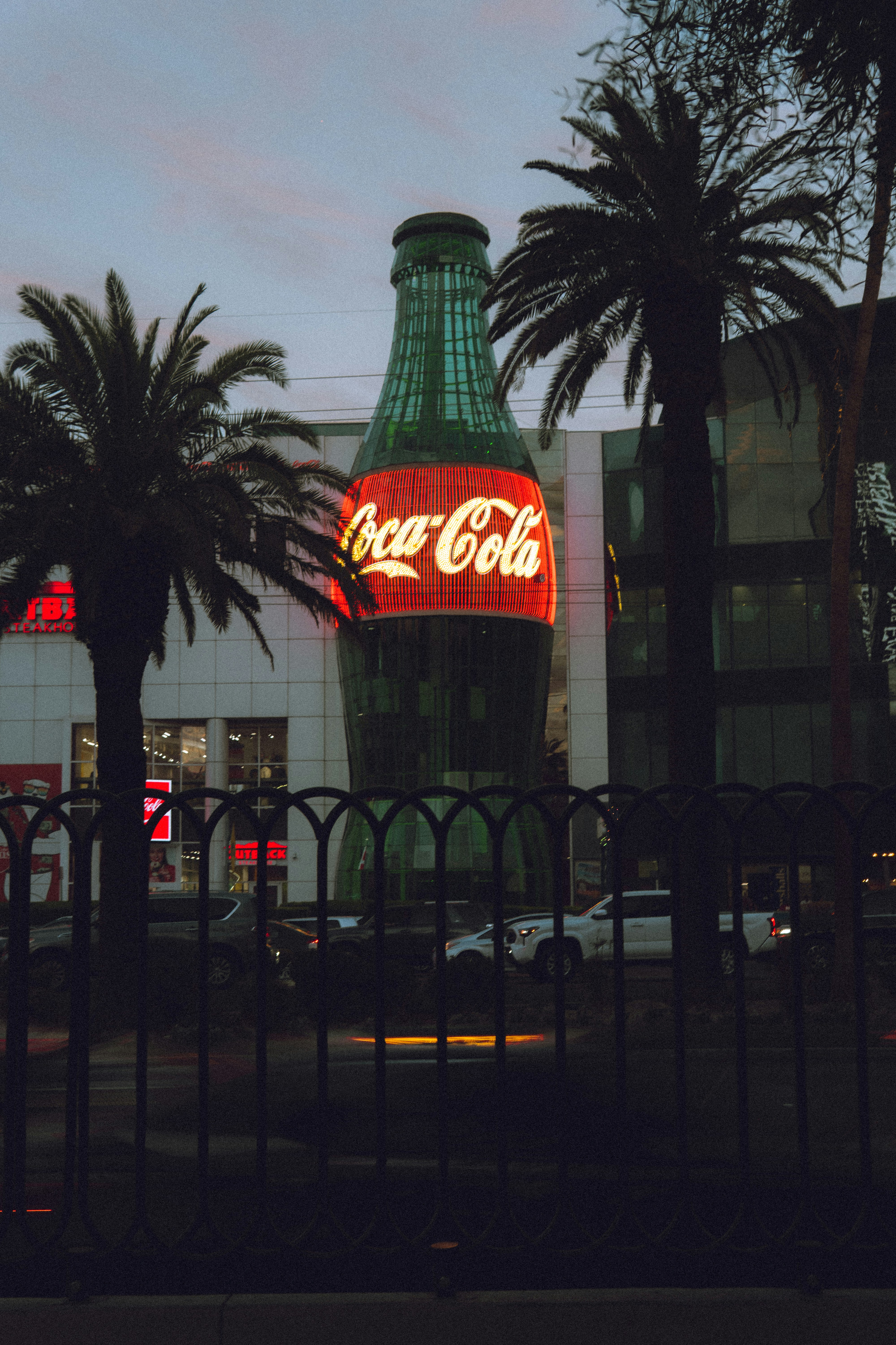 Neon Coca-Cola Giant bottle framed by palm silhouettes