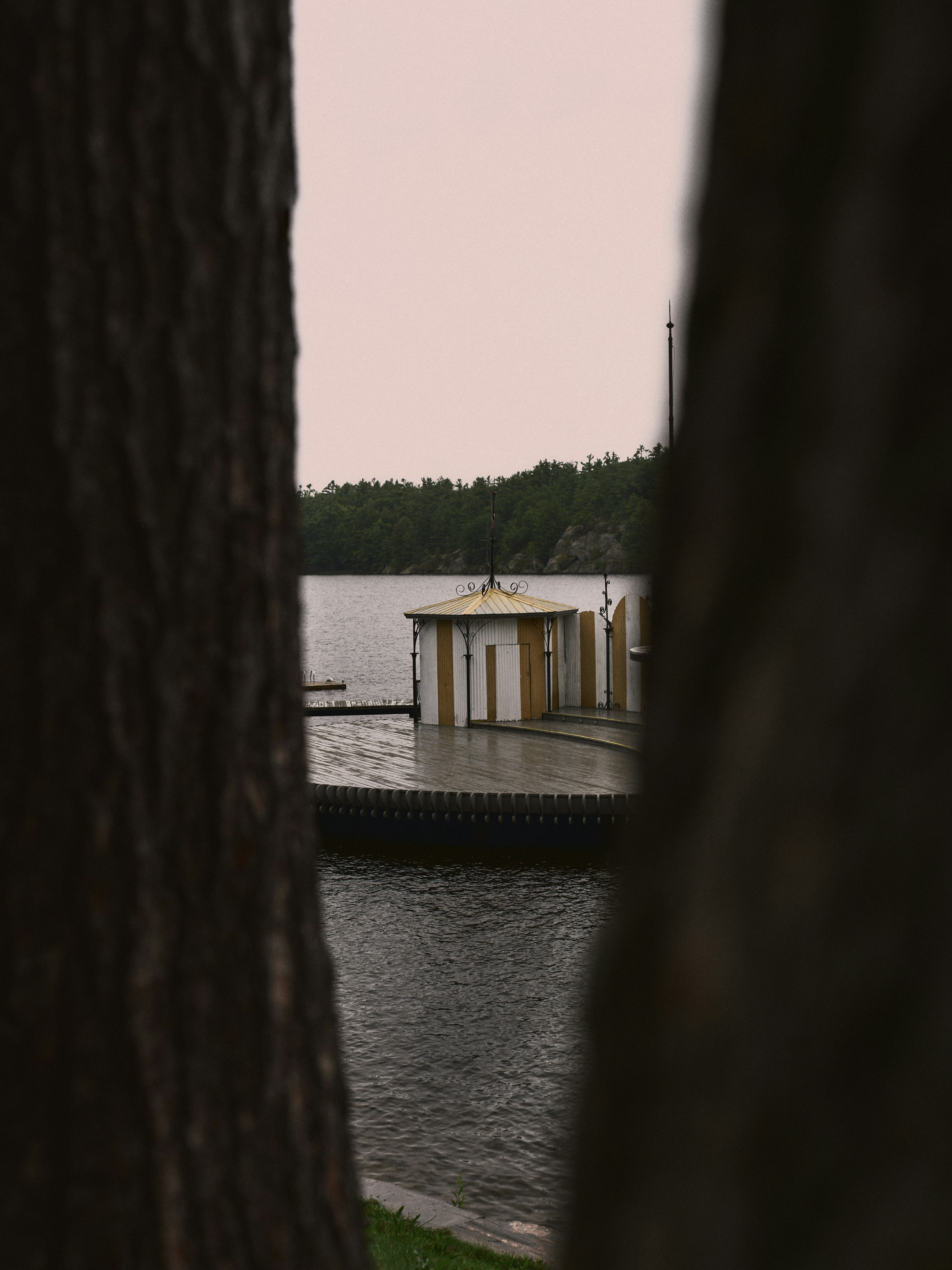 A striped wooden gazebo on a lake dock framed by two dark tree trunks