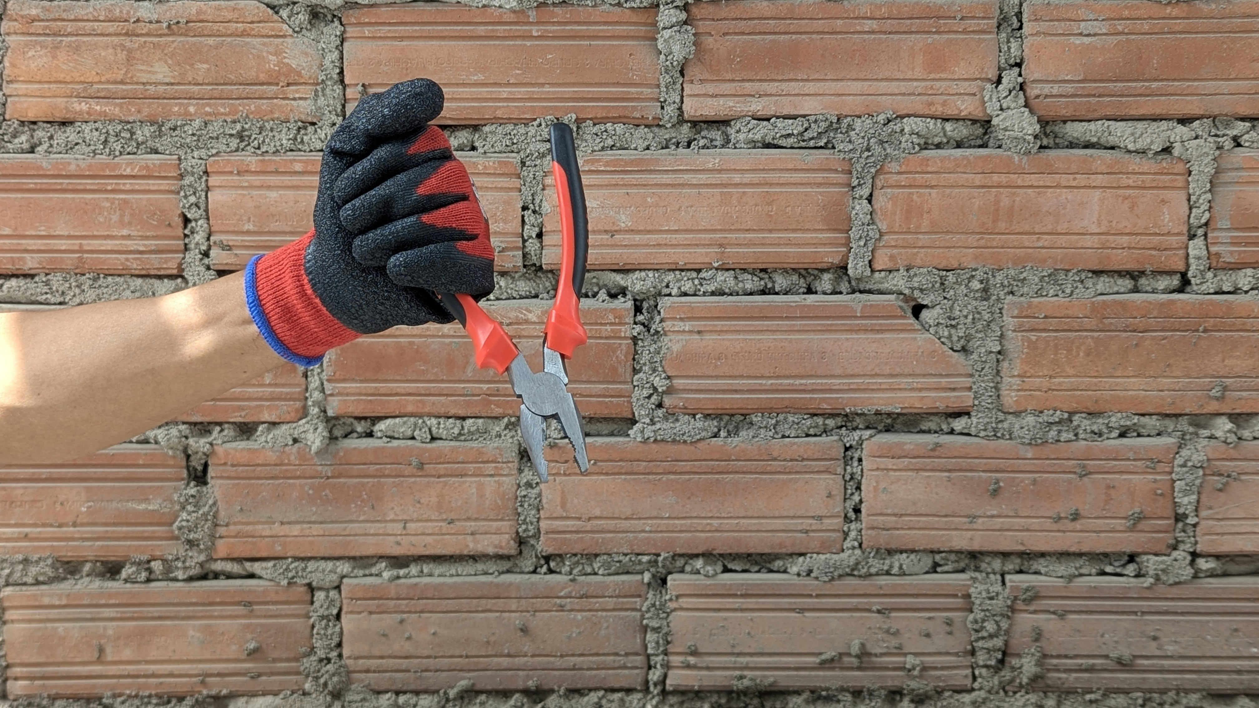 Tug of Tool: Hand and Snips in Front of Brick Pattern