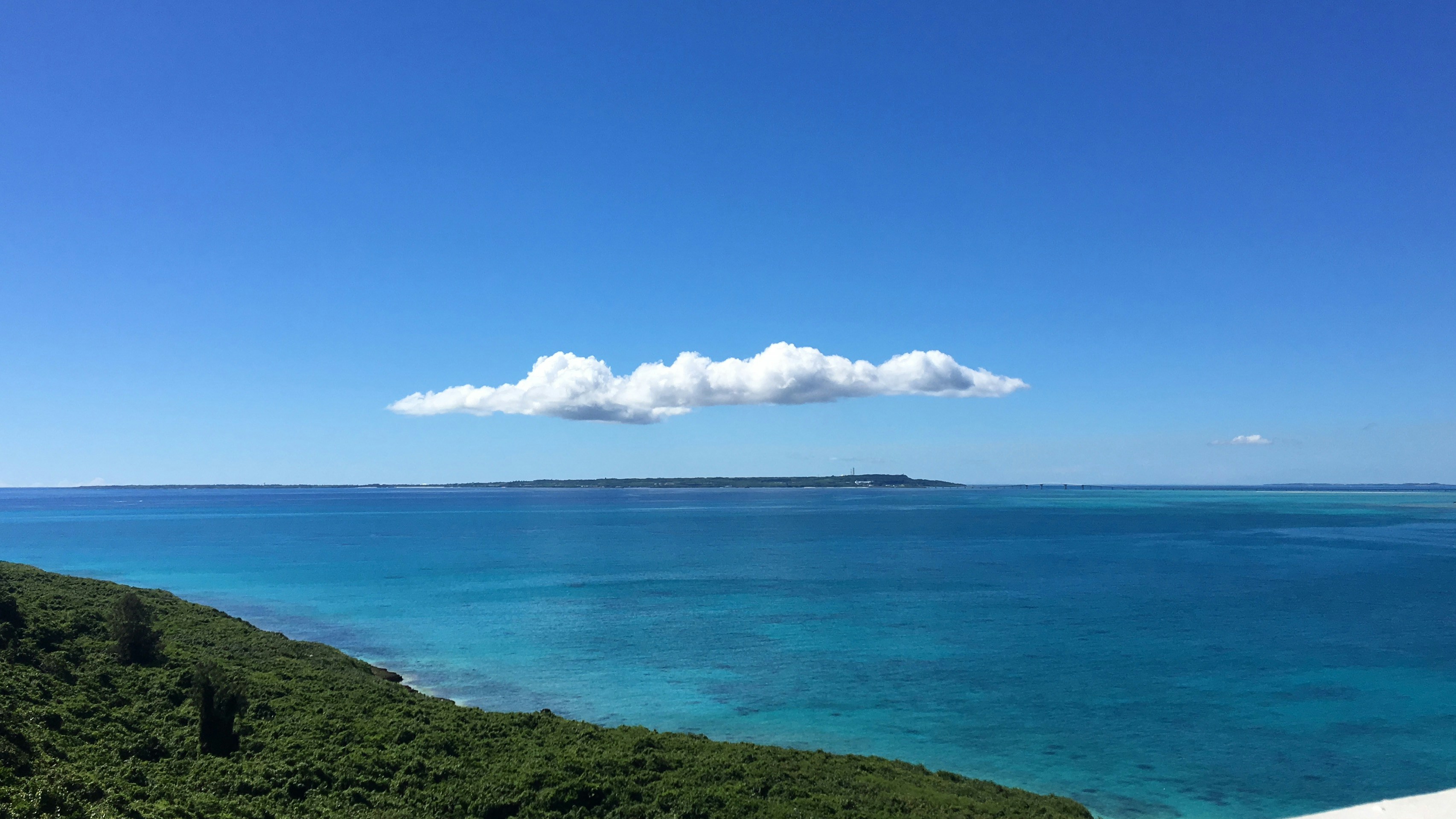 Calm coastal scene with a clear blue sea meeting a distant horizon and a single fluffy cloud above, capturing a tranquil seascape without people or vehicles.