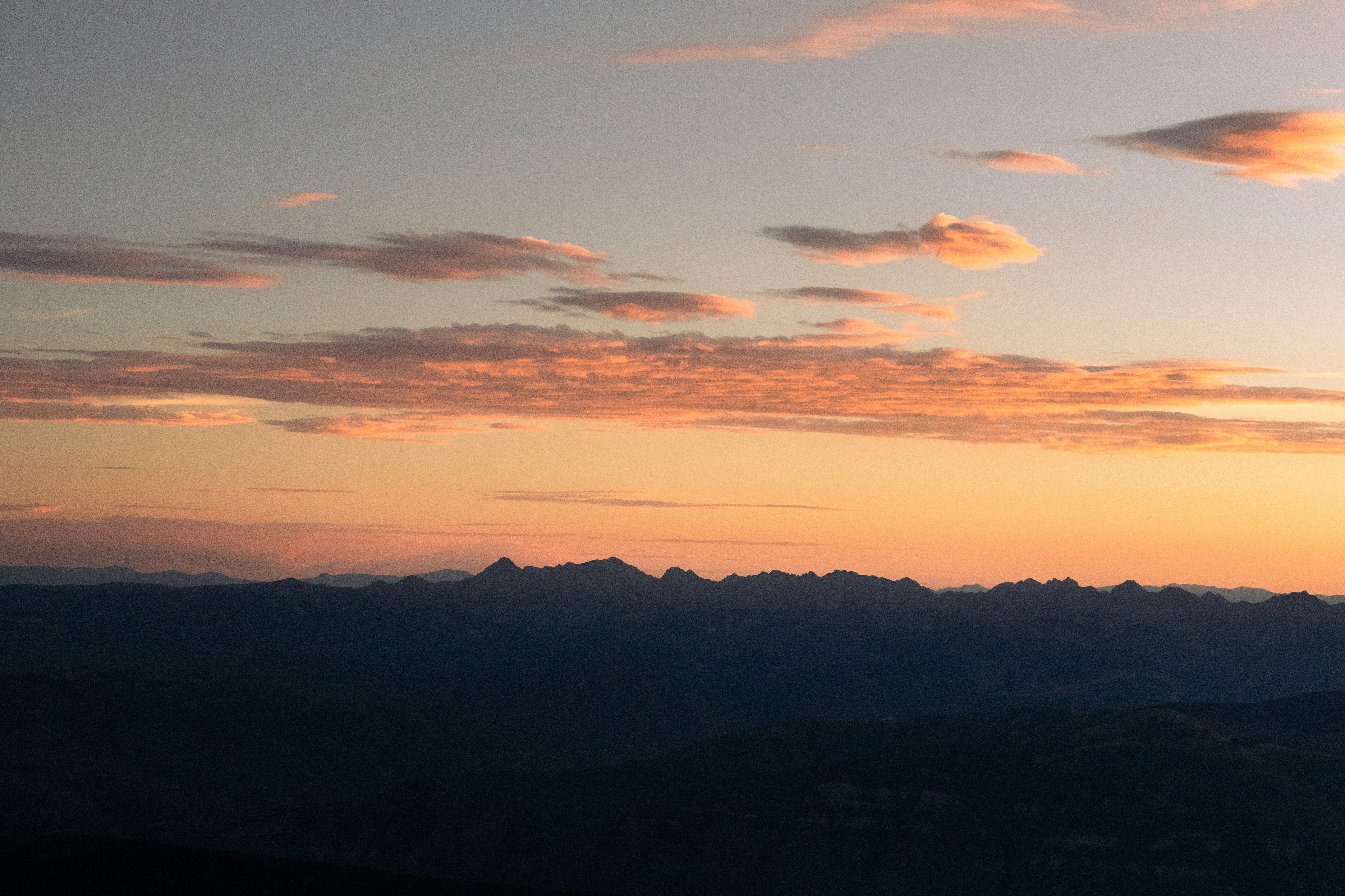 Soft sunset light over a layered mountain ridge with a calm, dark valley below; warm sky highlights and distant silhouettes convey quiet depth. (Landscape photograph)