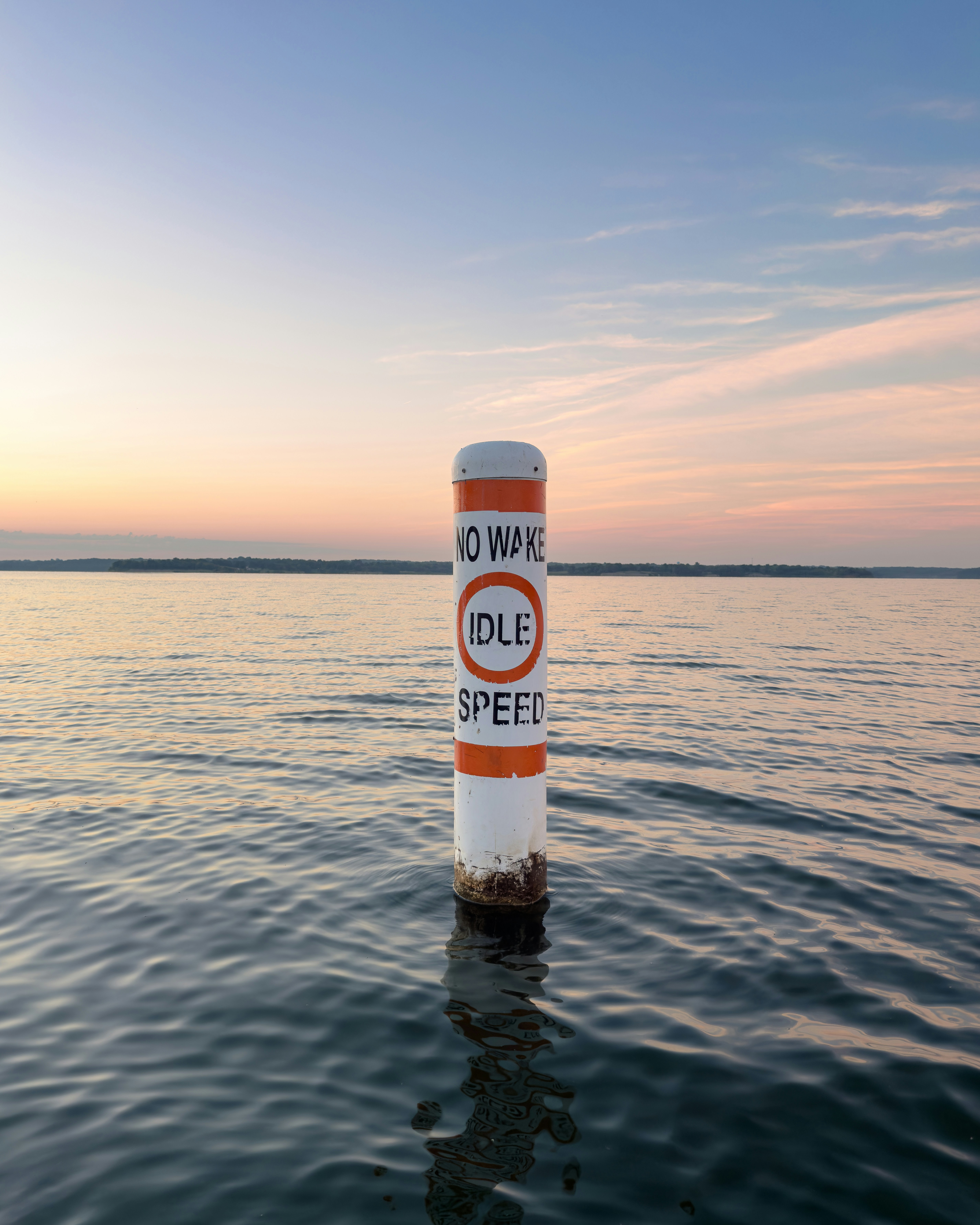 Colorful buoy rising from calm water at sunset, with a distant horizon and pink-orange sky.