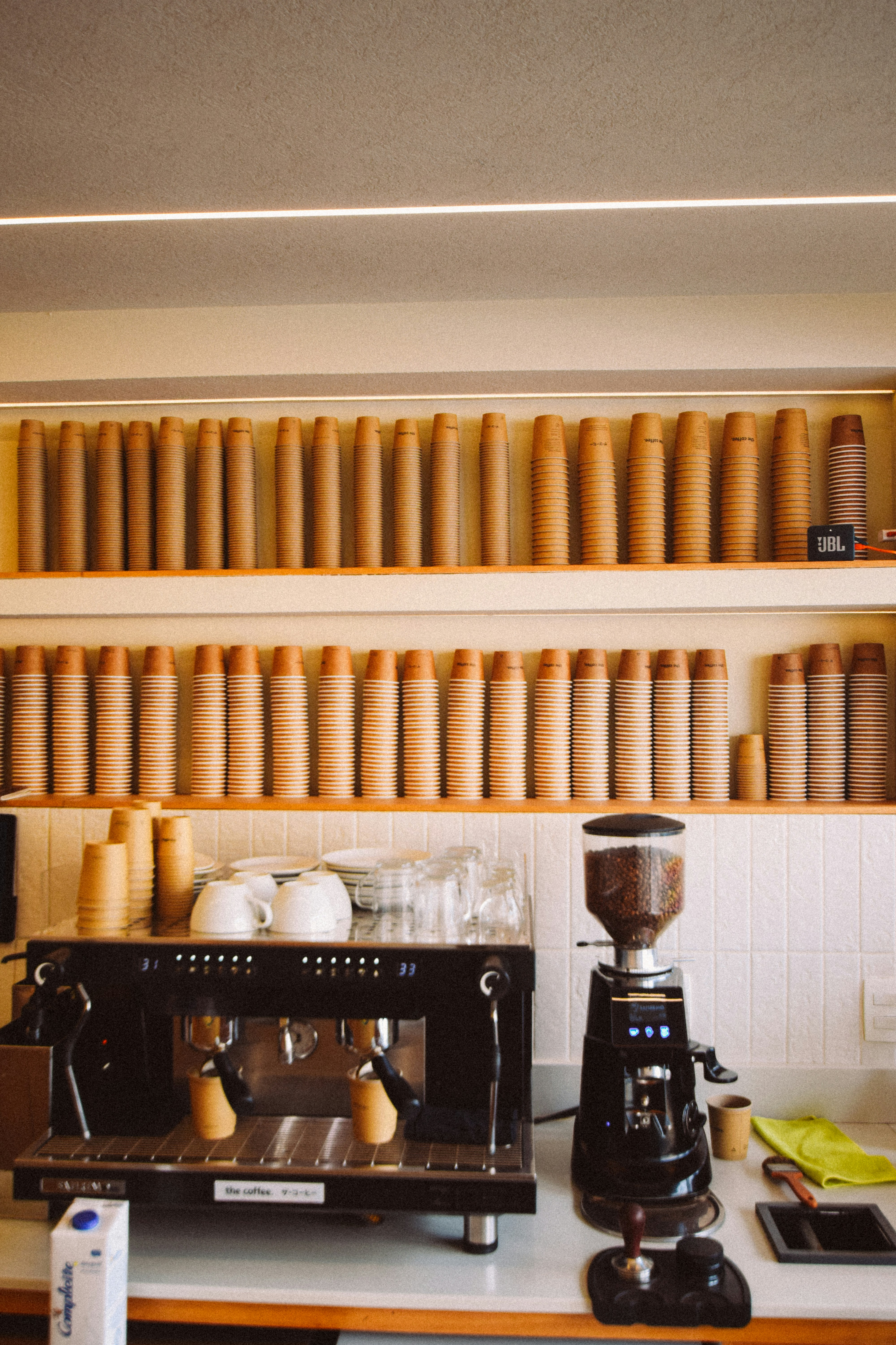 Row of brown disposable cups lining a coffee shop shelf with a coffee machine and grinder below