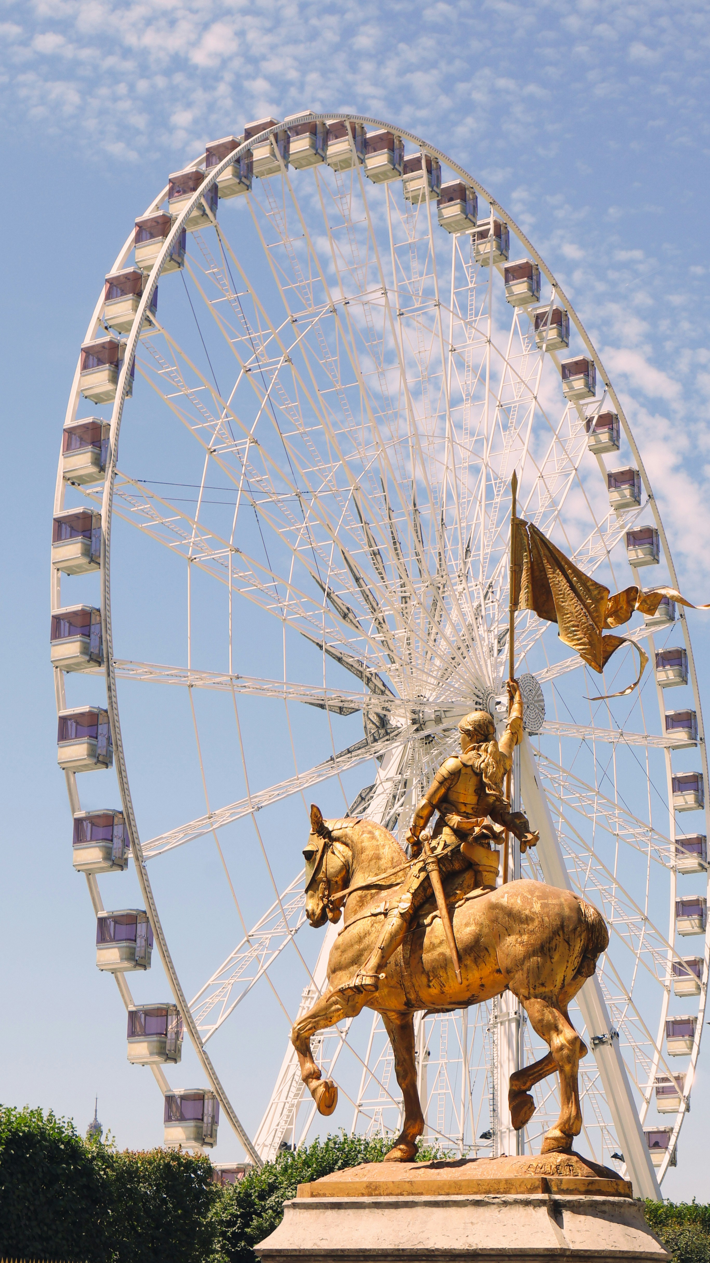 Bronze equestrian statue in the foreground with a towering Ferris wheel against a blue sky, creating a dramatic contrast between sculpture and amusement-park architecture.