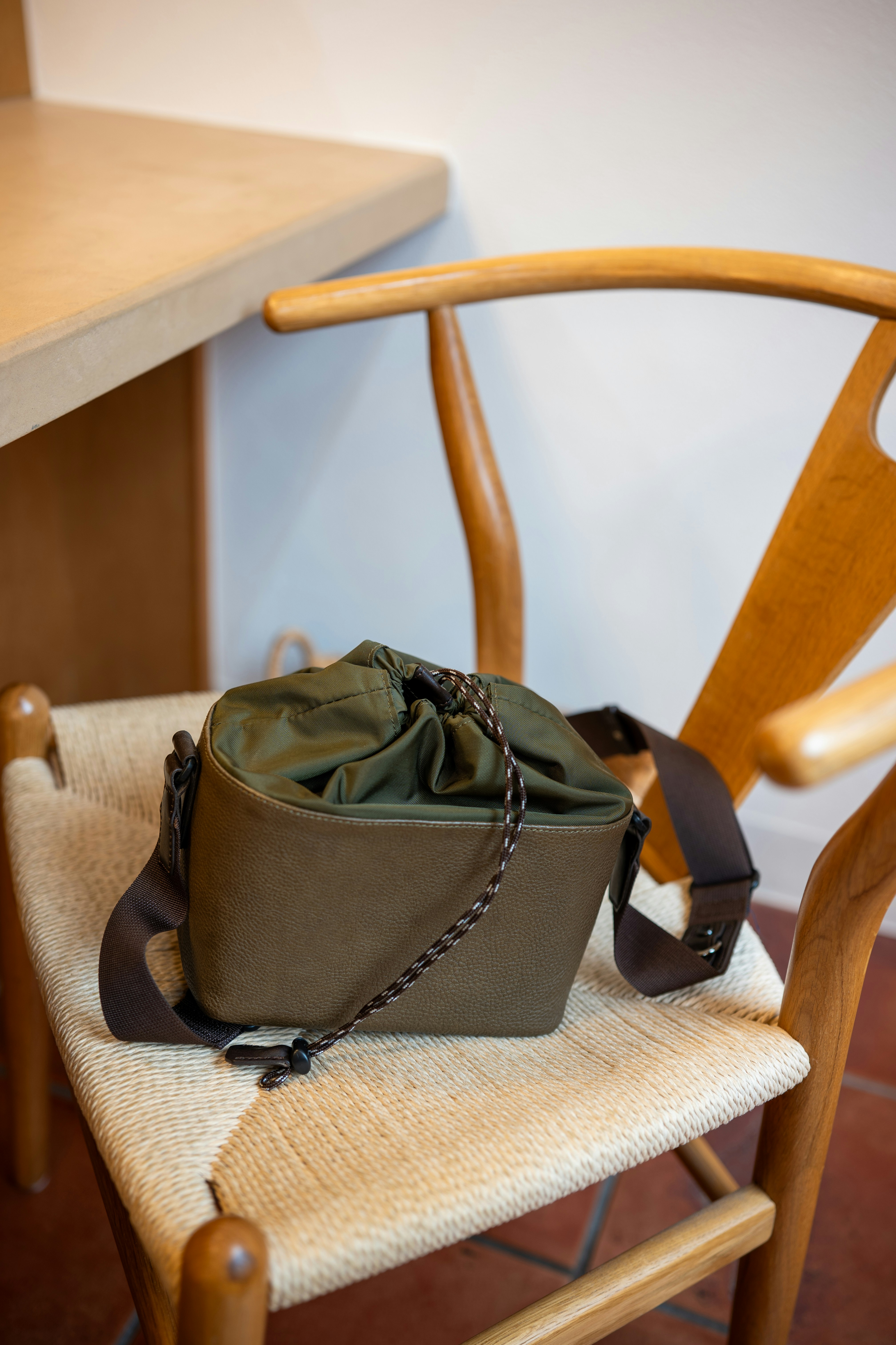 Olive field bag resting on a woven chair in a sunlit room