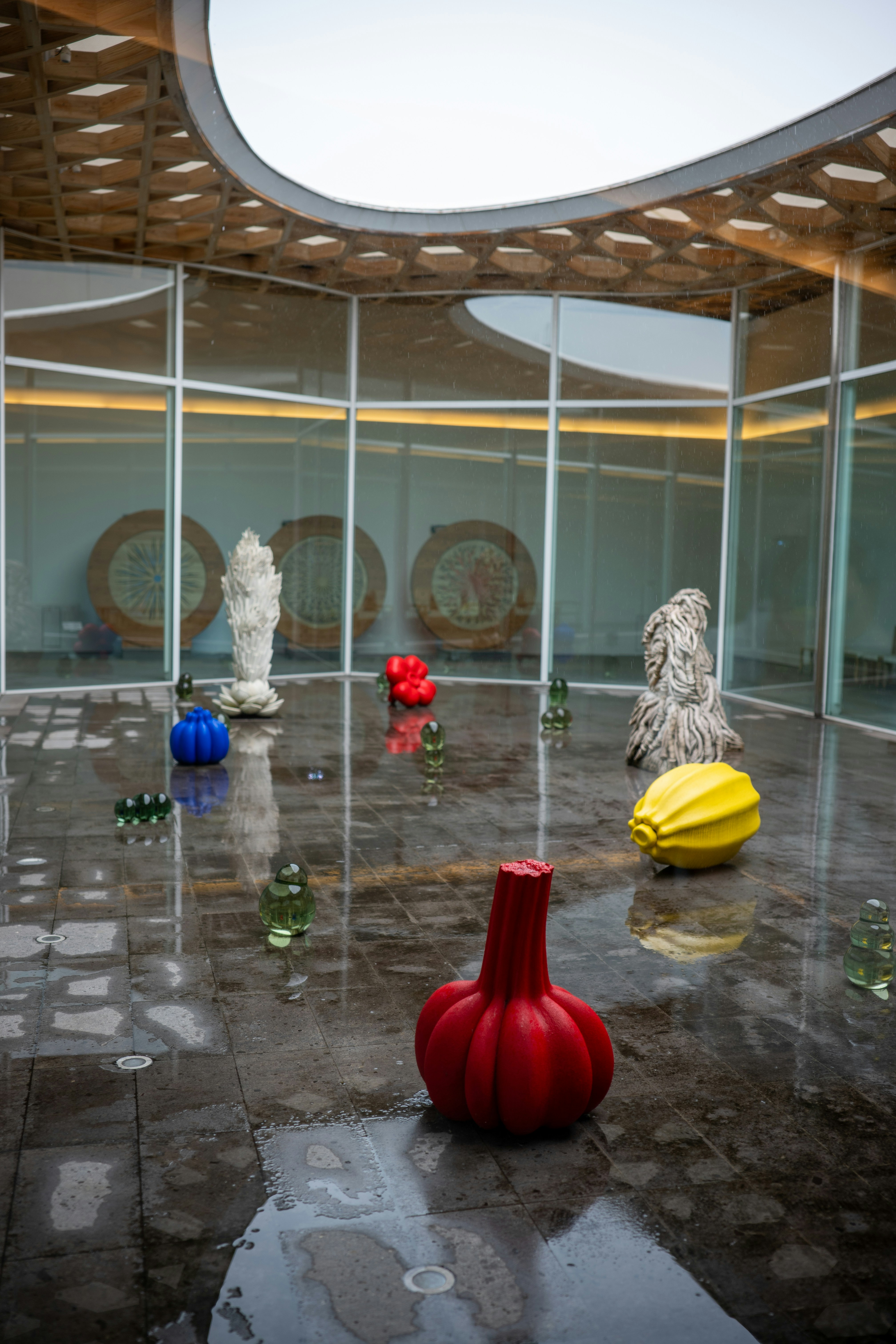 Colorful Sculptures on a Wet Gallery Floor Under Circular Skylight