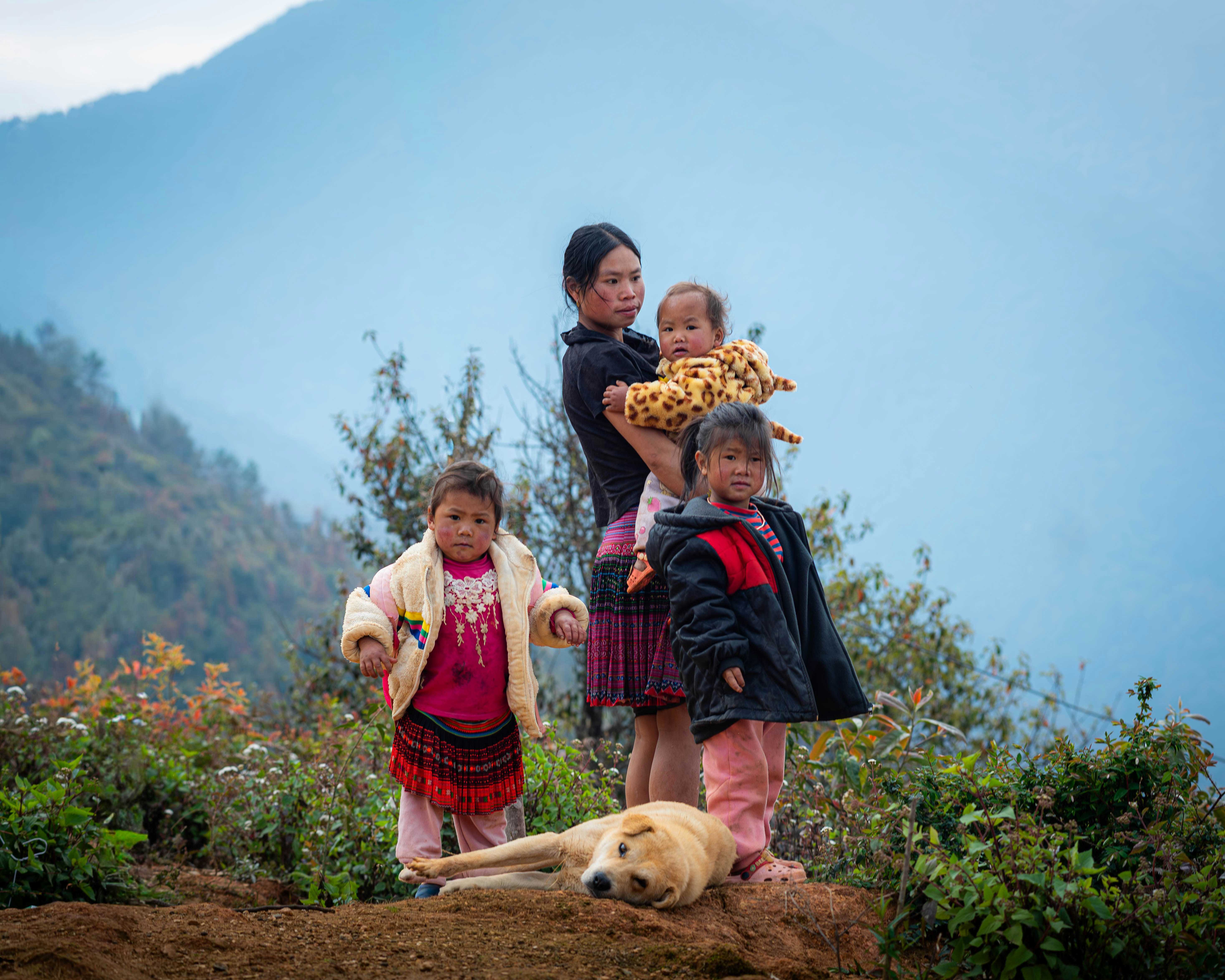 Mother with three children and a reclining dog against a blue-hazed mountain backdrop