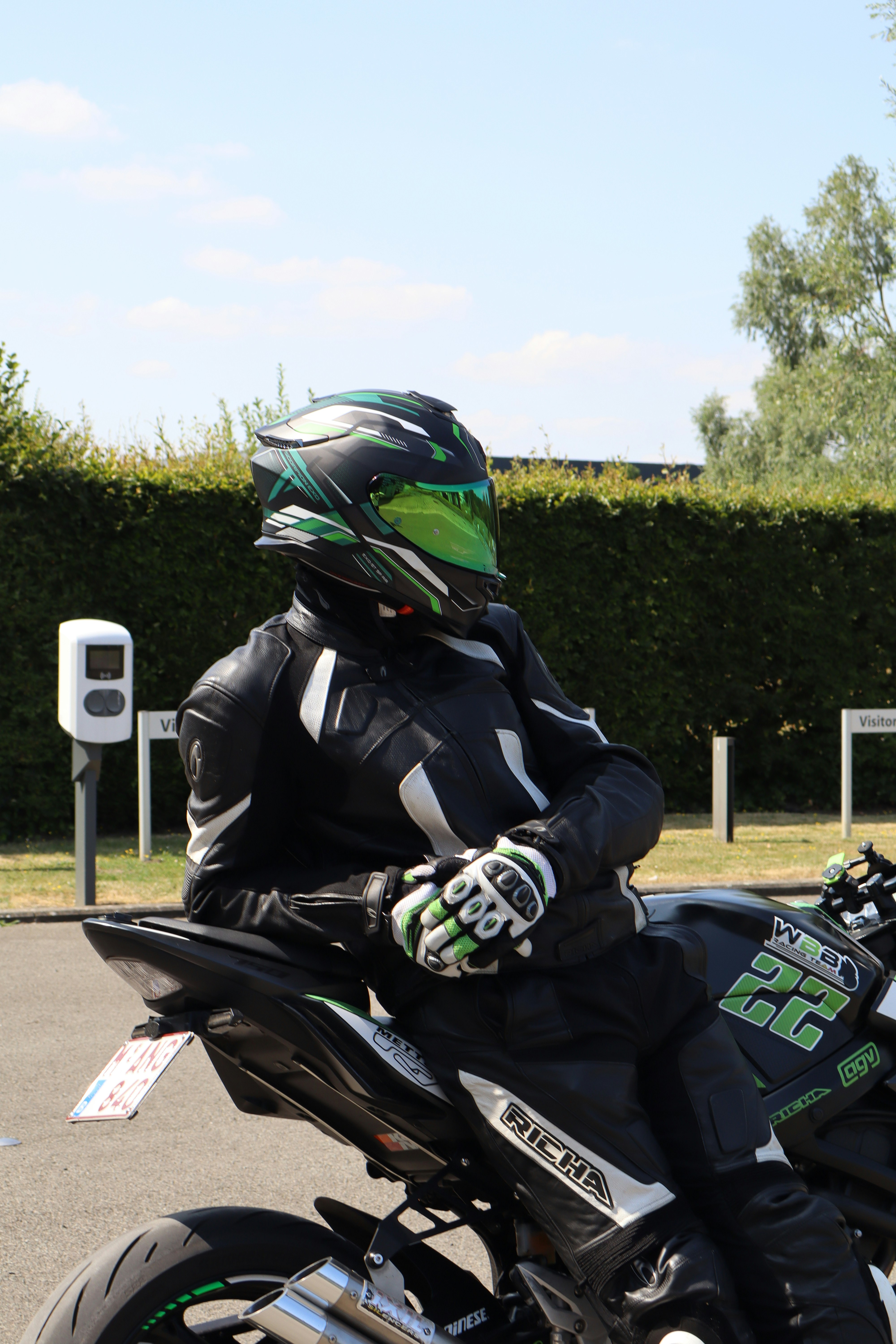 Rider in black and white gear on green-lamed sportbike at a parking lot