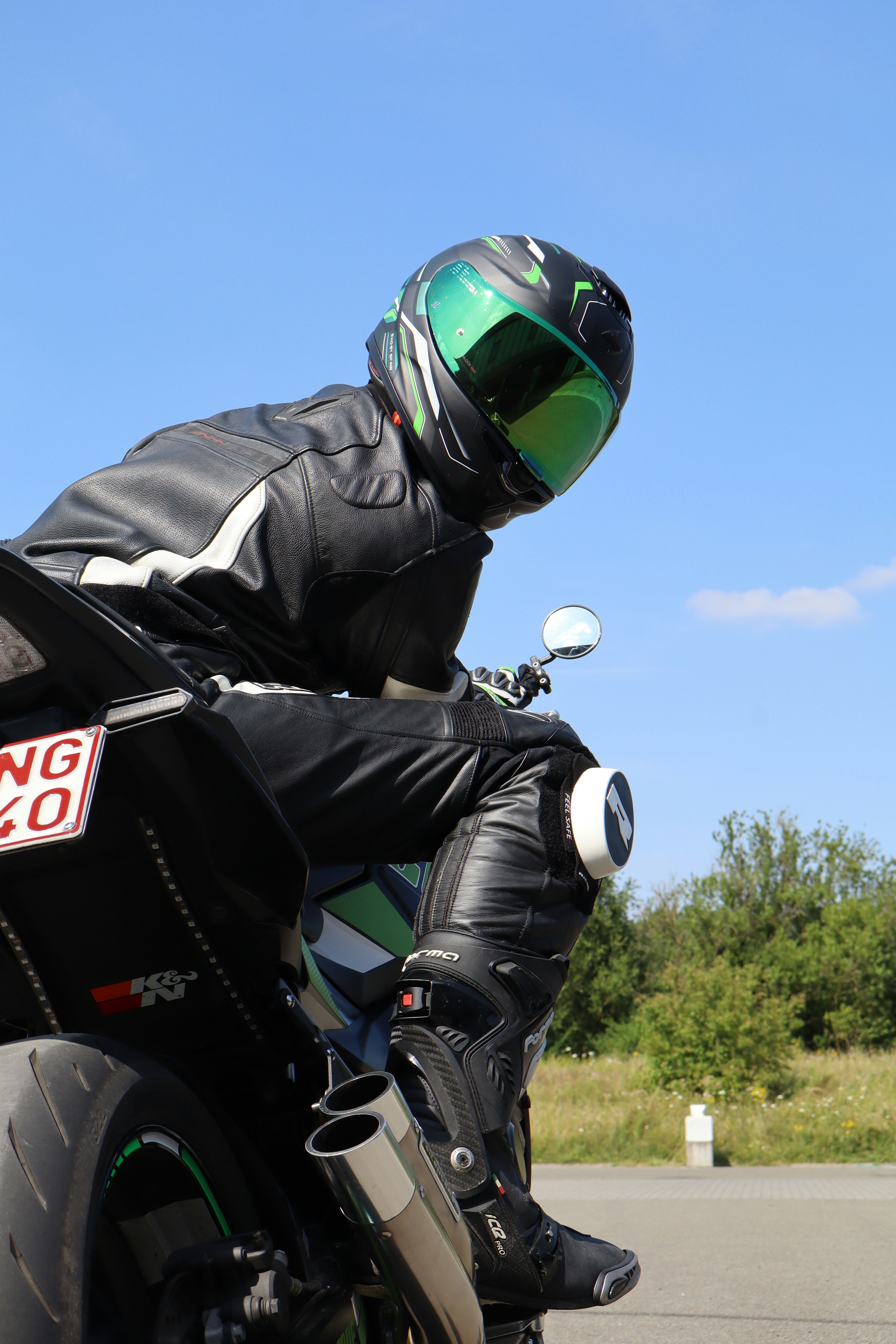 Rider in full protective gear on a sportbike, blue sky backdrop and a roadside patch in the distance. A foreground action shot emphasizing motion and motorcycle details.