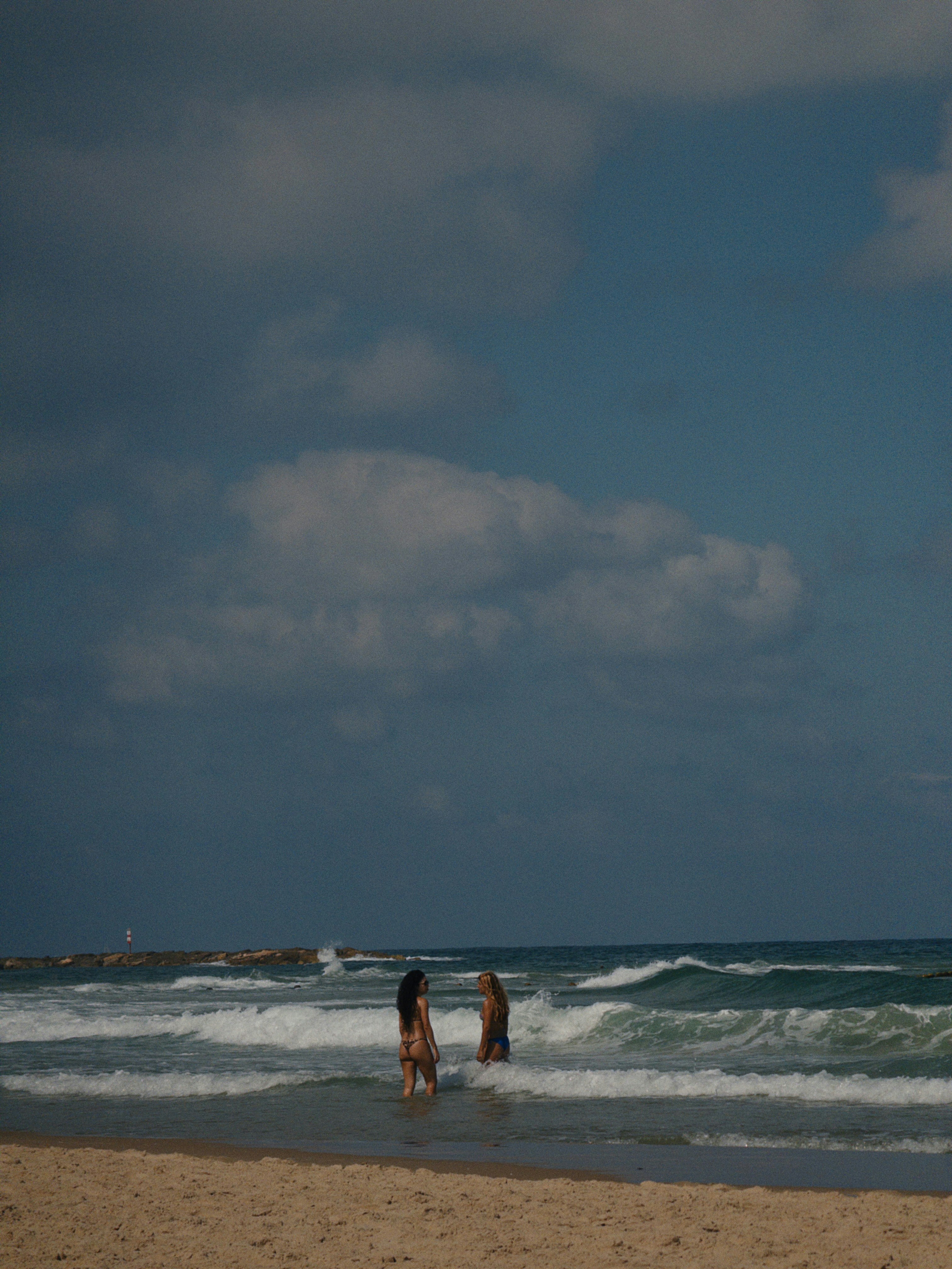 Two Beachgoers in Gentle Surf Under Overcast Sky