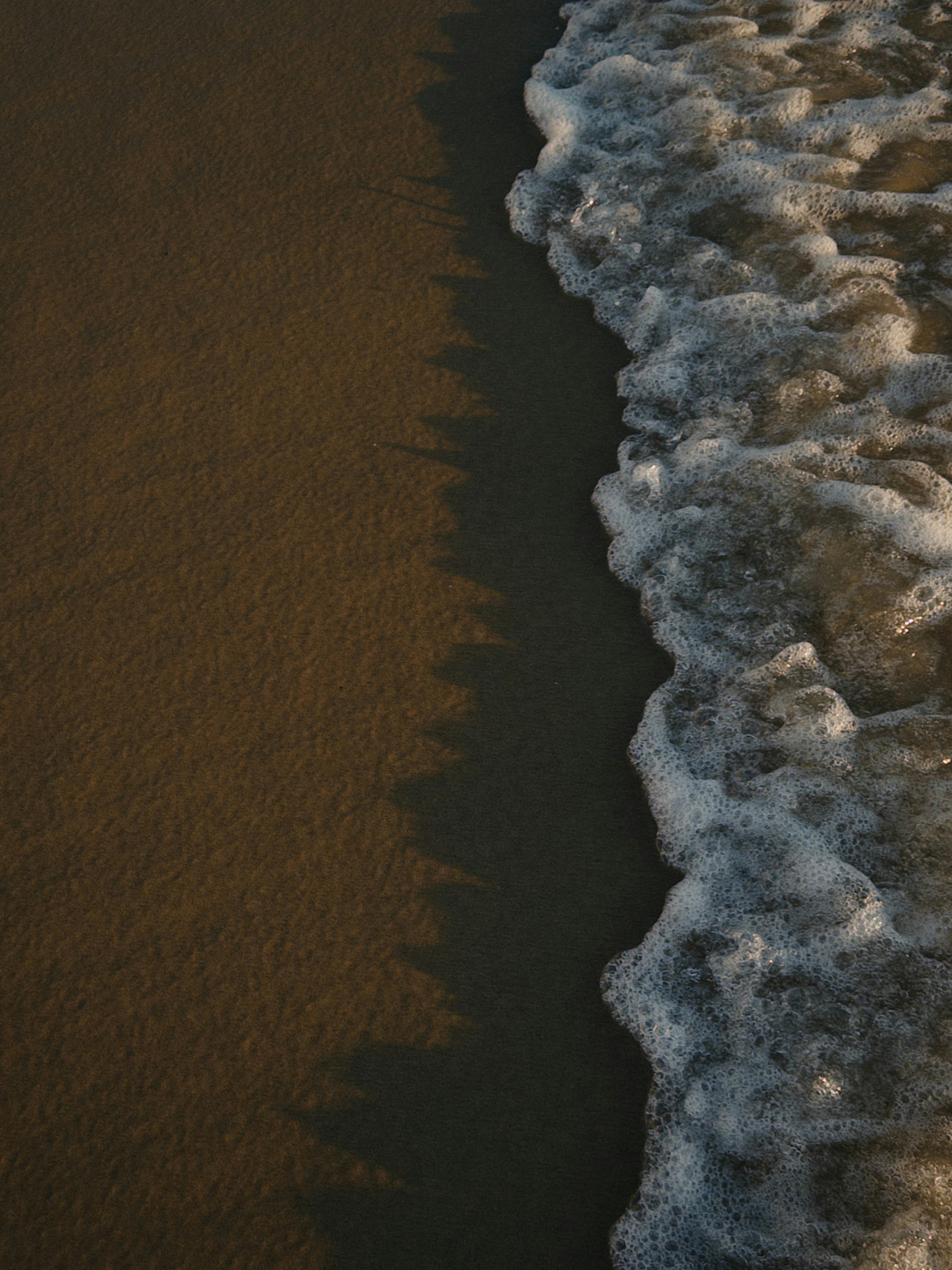 Foamy shoreline shifting from dark wet sand to white lace at the edge of breaking waves