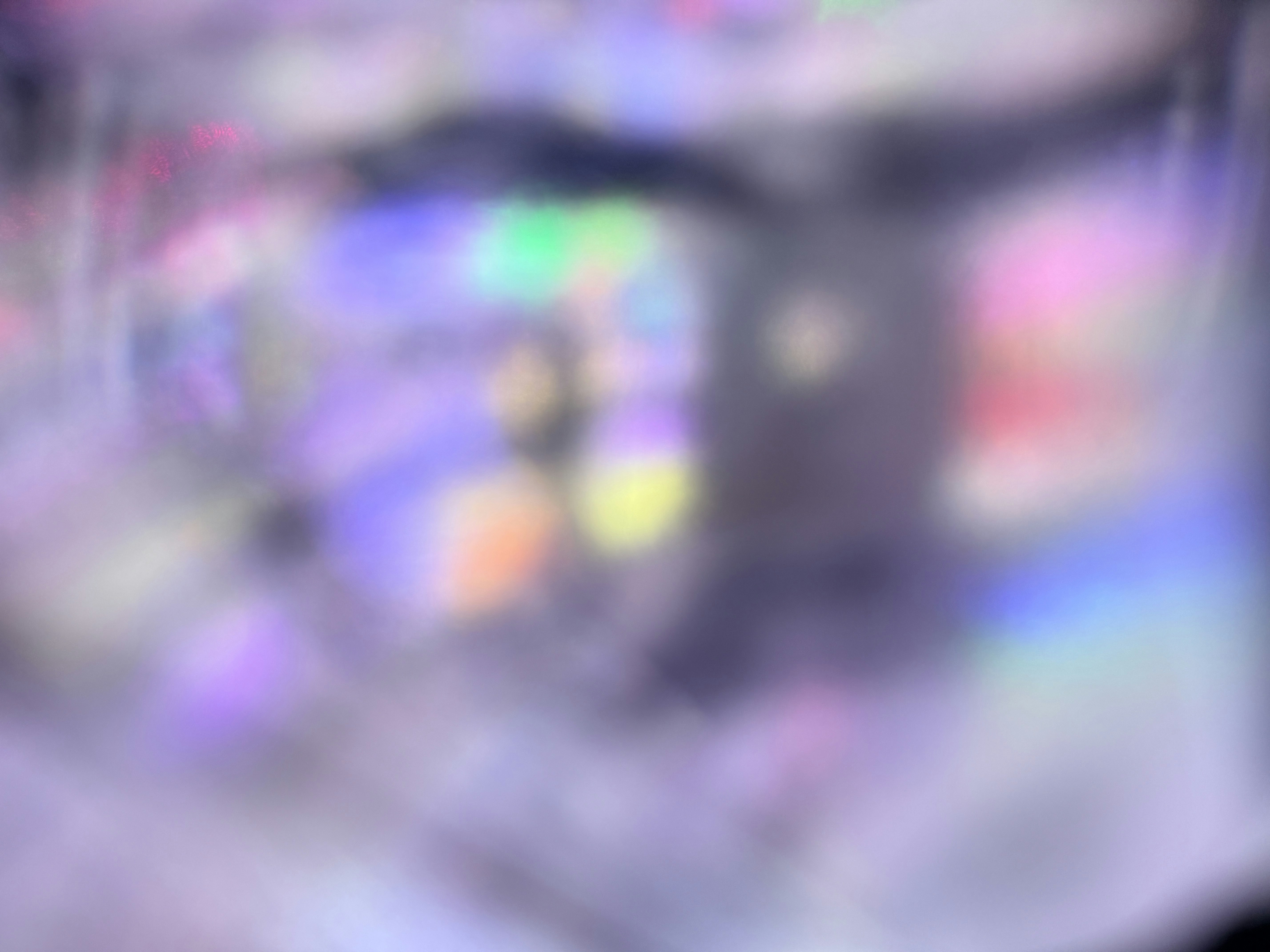 Neon-lit stage blur with colorful bokeh and indistinct figures in a concert-like setting. Abstract, high-gloss atmosphere with vibrant lights and soft focus.