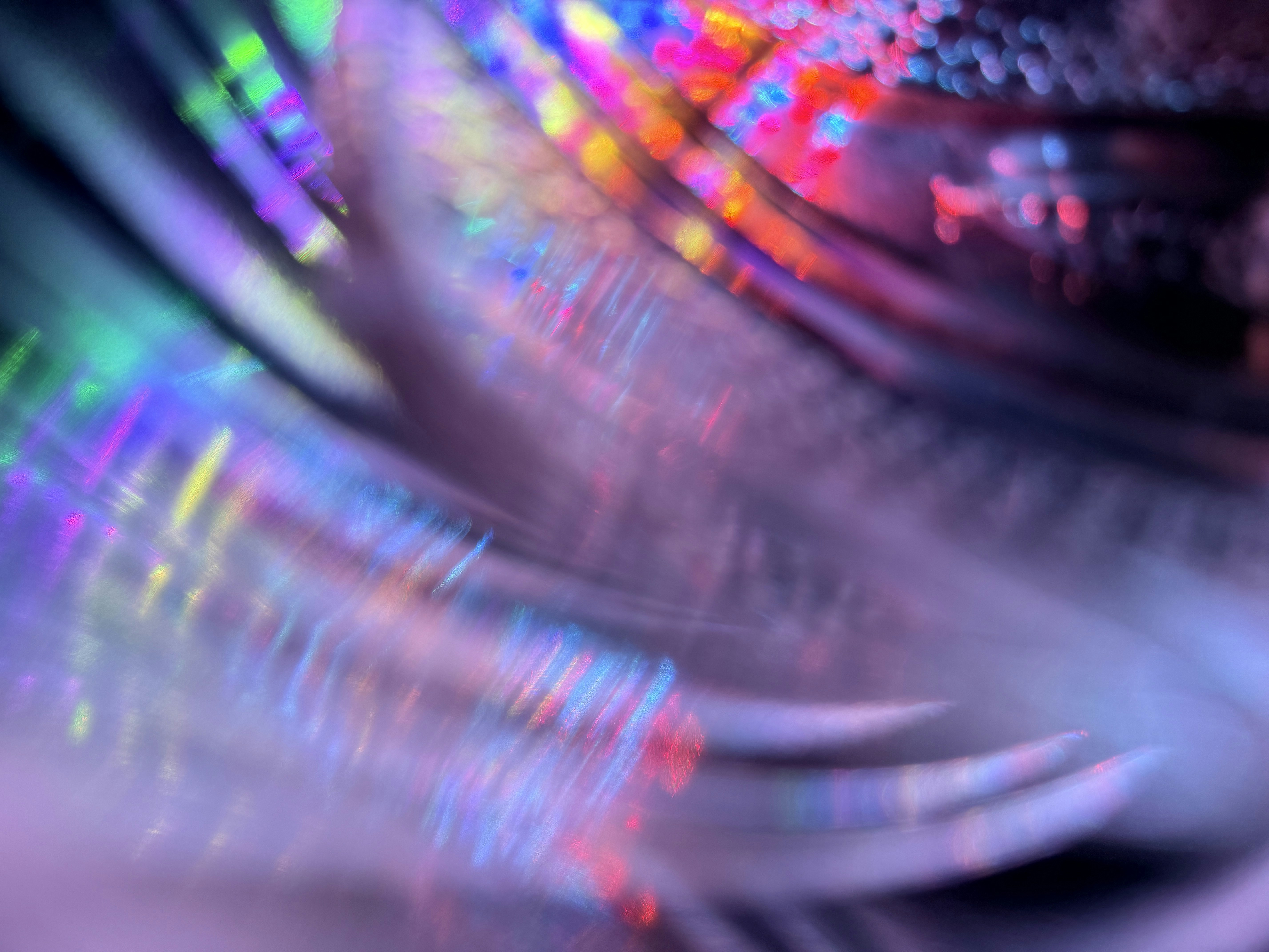 Abstract macro-inspired light swirls and prism shards create a kaleidoscopic glow with rich color, suggesting motion and texture. A non-figurative, artful capture emphasizing color dispersion and lens reflections.