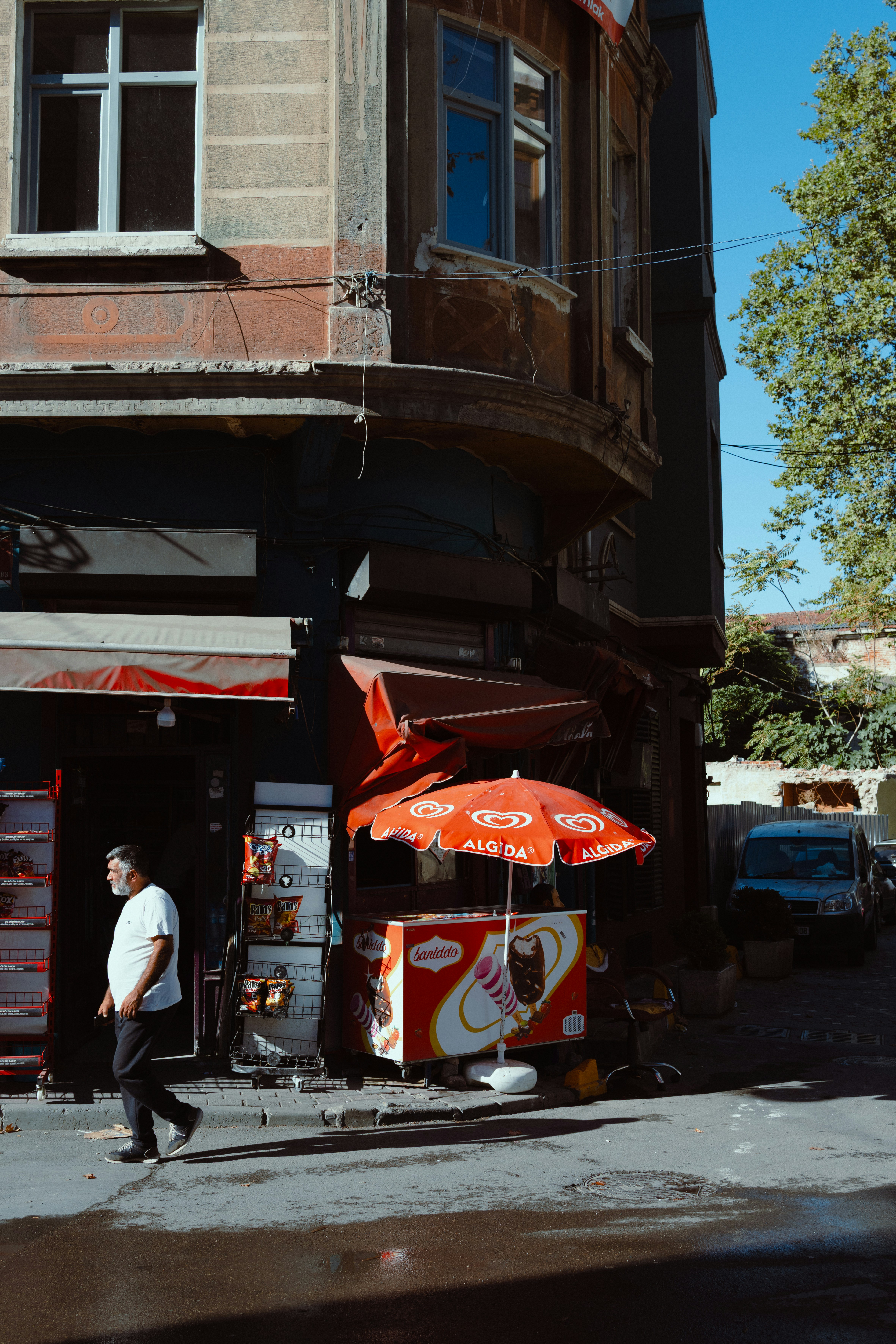 Sunlit Corner Shop with Orange Ice Cream Stand Under a Warm, Aged Brick Building