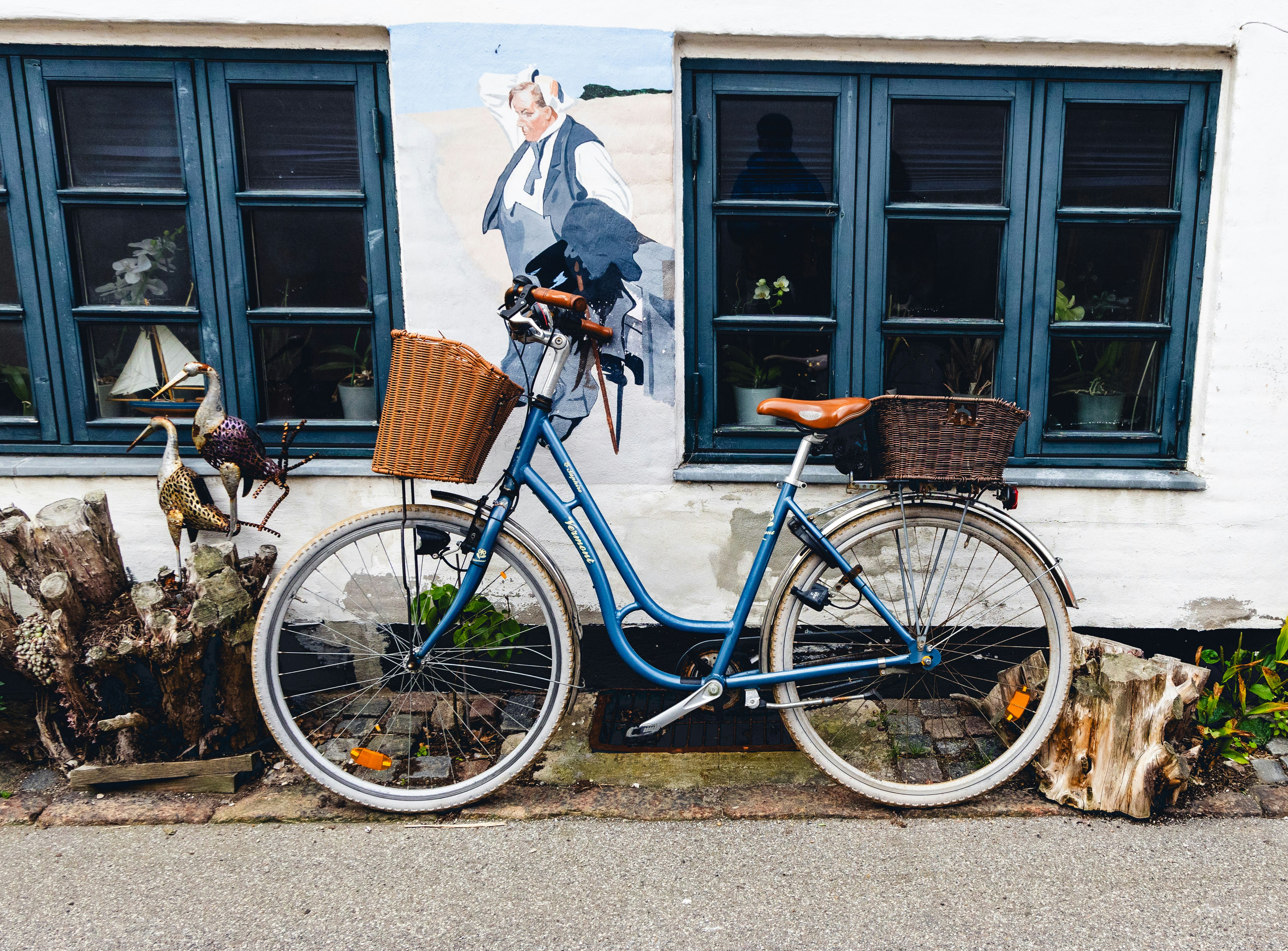 Blue bicycle with wicker baskets against a muraled wall