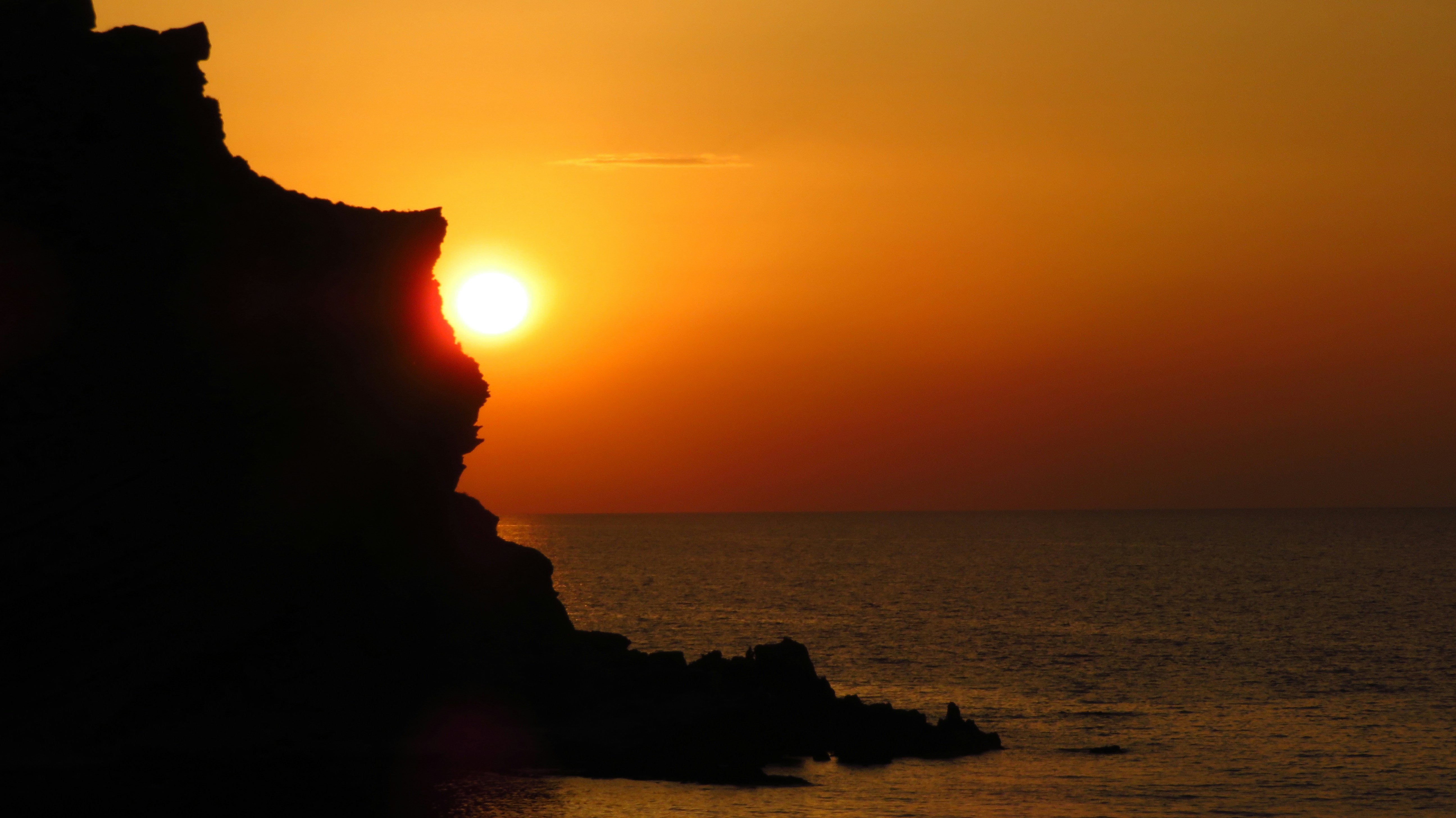 Silhouette at Dusk: Sun Nestled Against a Cliff Edge
