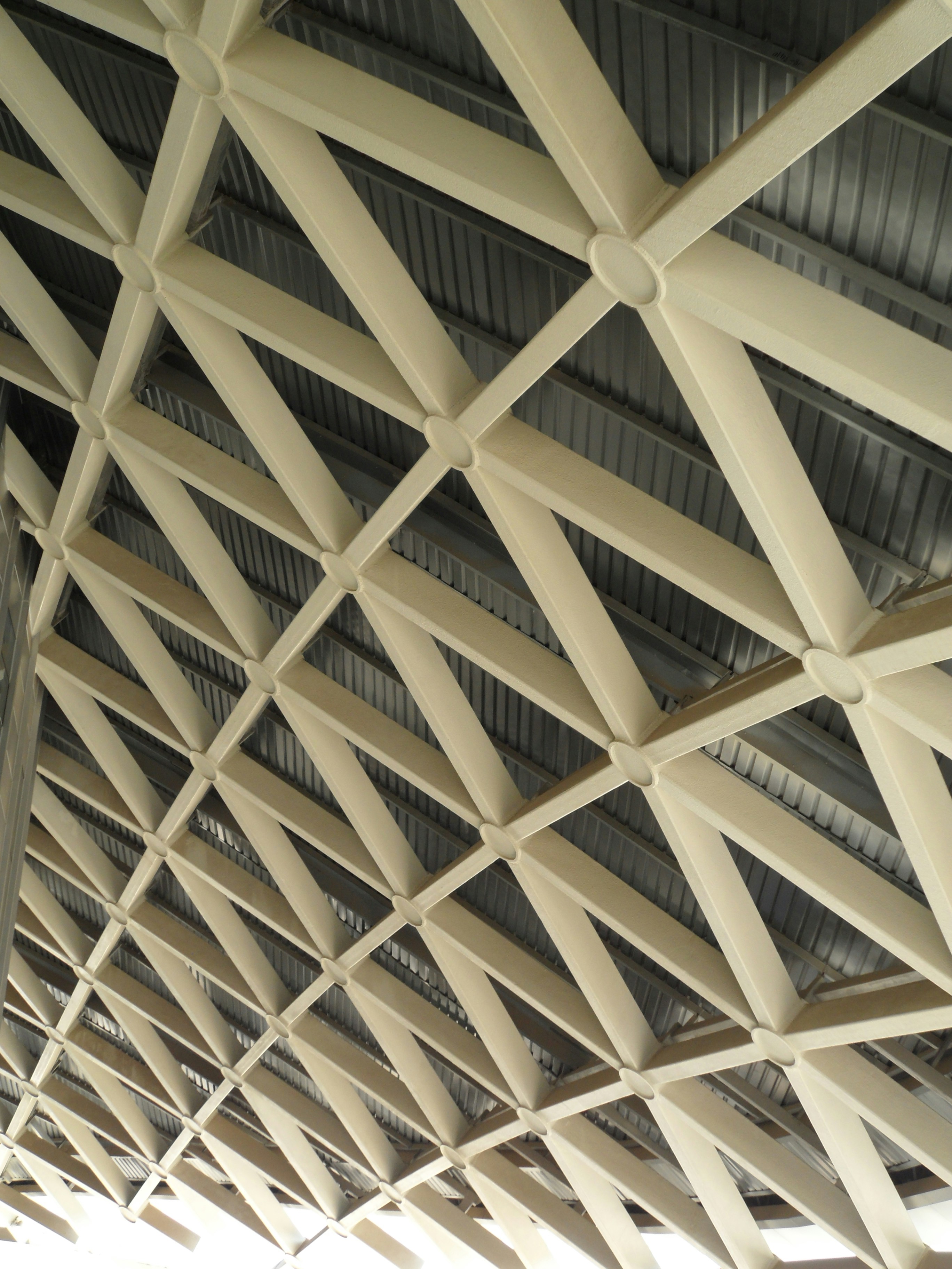 Architectural lattice of interlocking beige beams forms a repeating triangular pattern across the frame. The image emphasizes structure and rhythm in industrial design.
