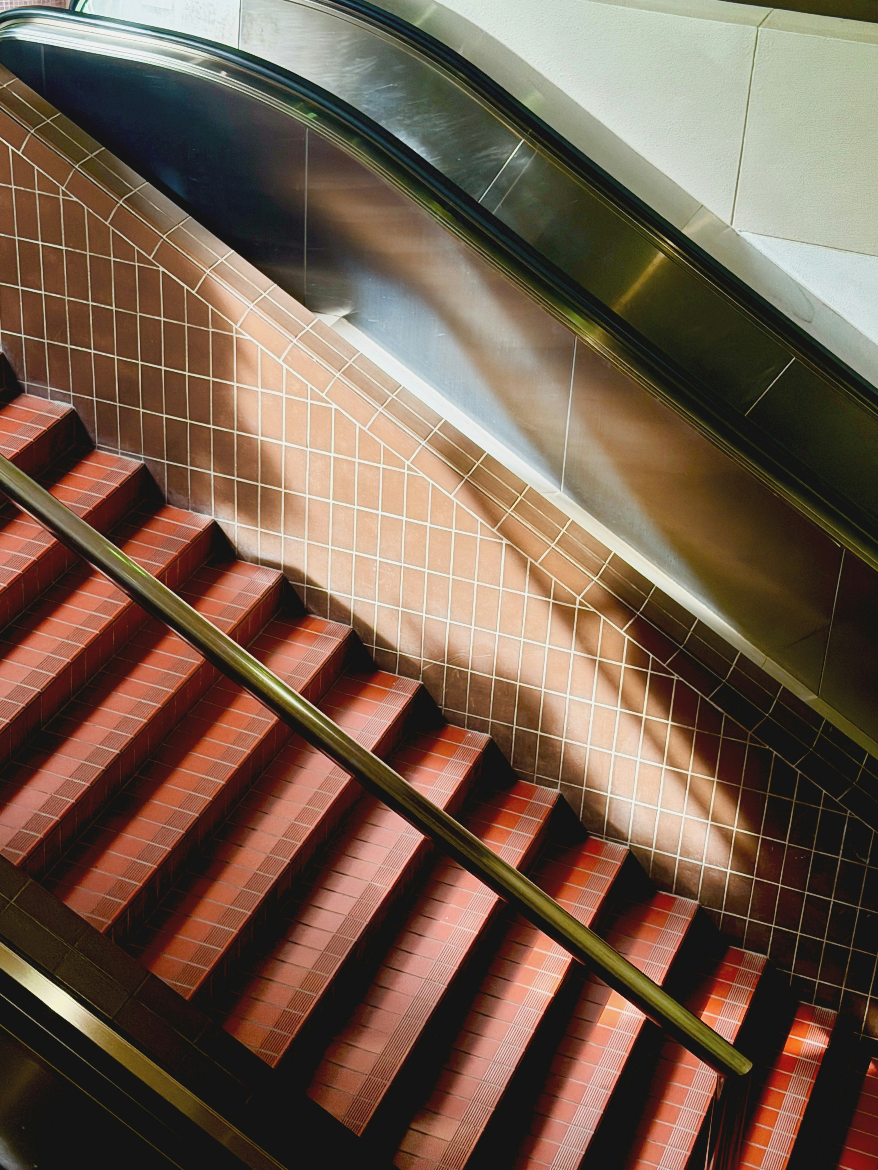 Indoors escalator with red-tiled steps and metal handrails, photographed at a tilted angle to emphasize motion and lines. This is a photographed scene, not a drawing.