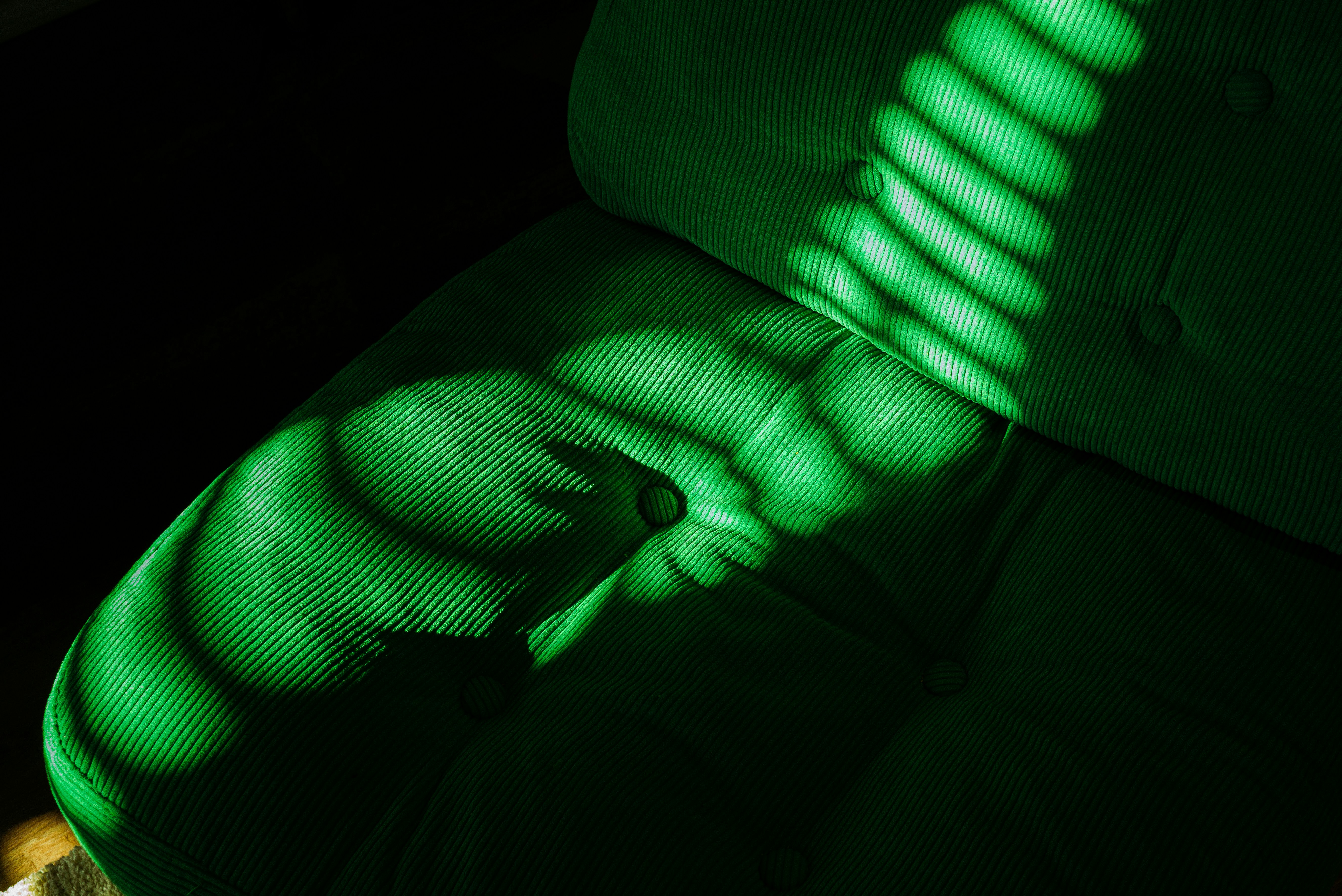 Bright green cushioned seat bathed in patterned sunlight, revealing textured fabric and overlapping shadow rings; minimal, indoor scene with emphasis on color and texture of the chair.