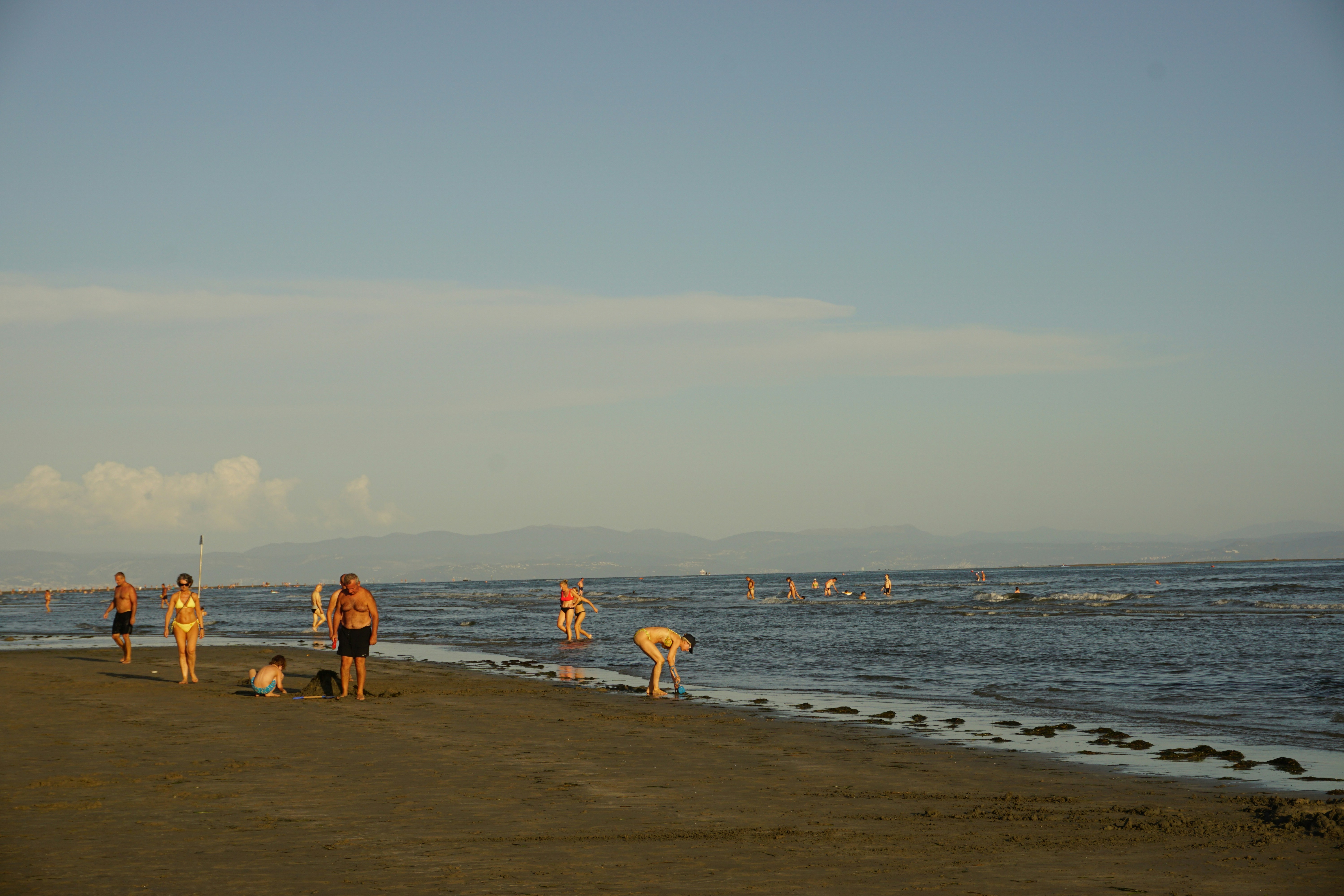 Sunlit shoreline: families and swimmers dot the calm sea