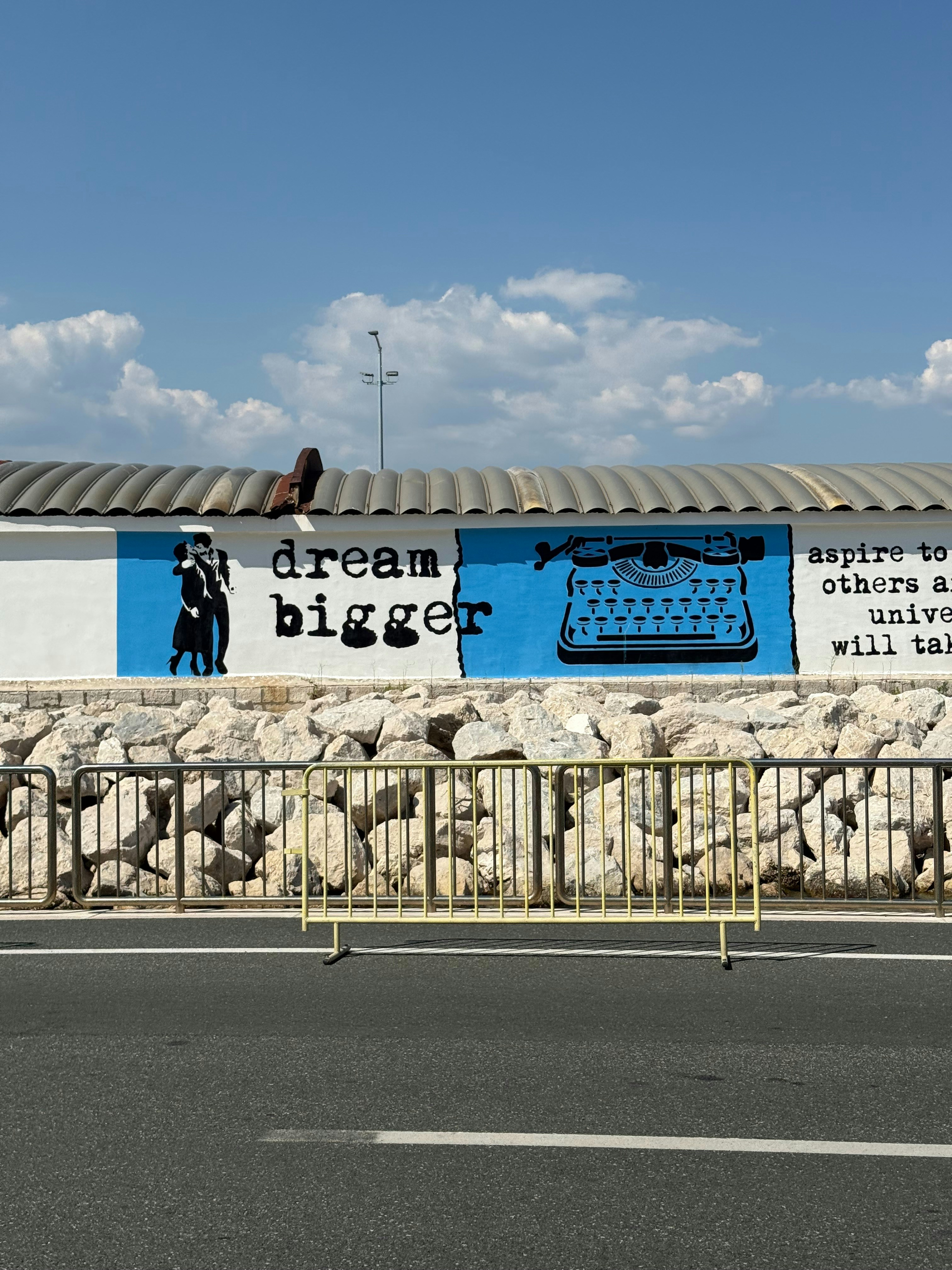 Blue mural of a dreamer and a typewriter along a seaside barrier