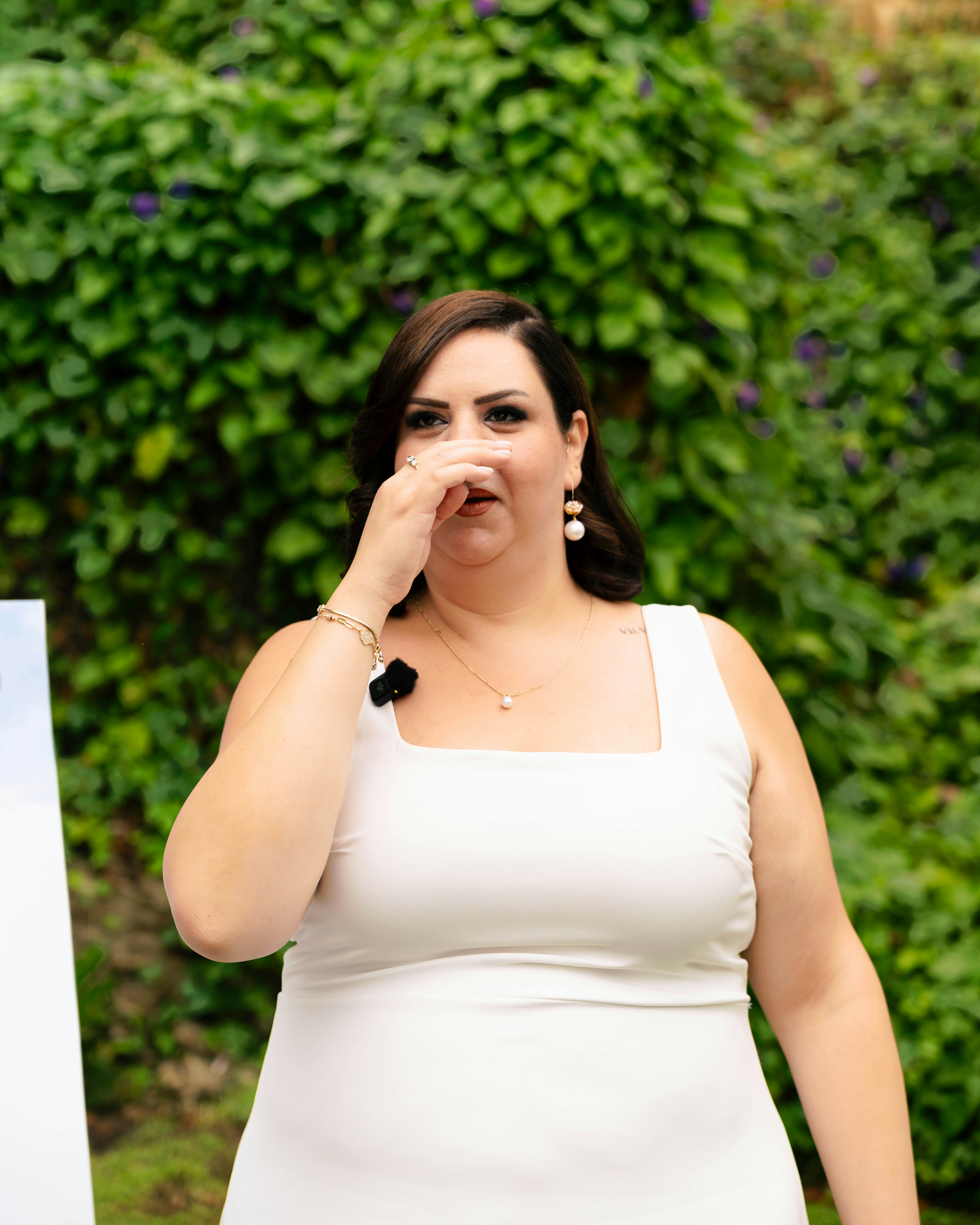 White‑dress portrait with candid gesture against a lush green backdrop
