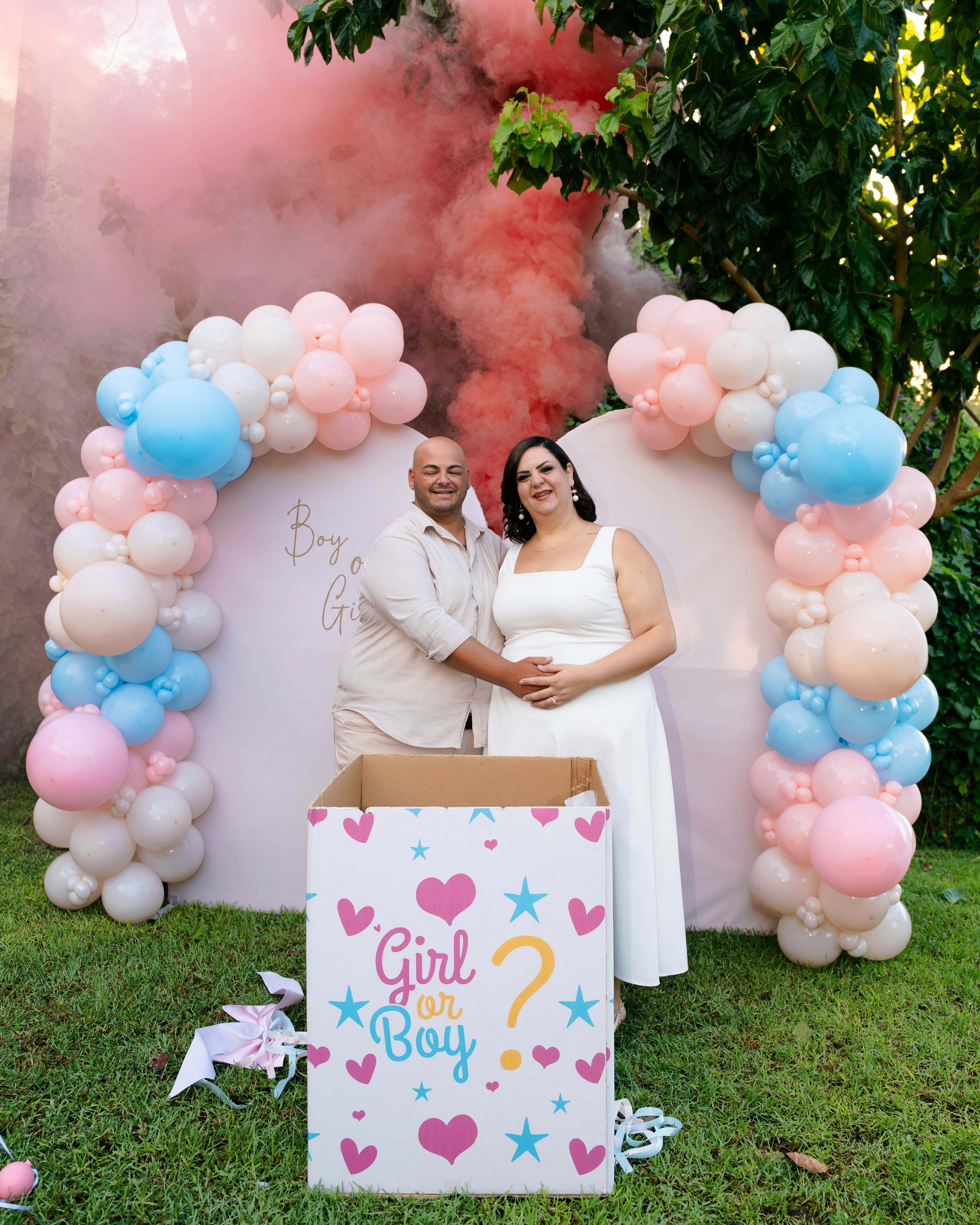 Gender reveal joy under pastel balloon arch with confetti box