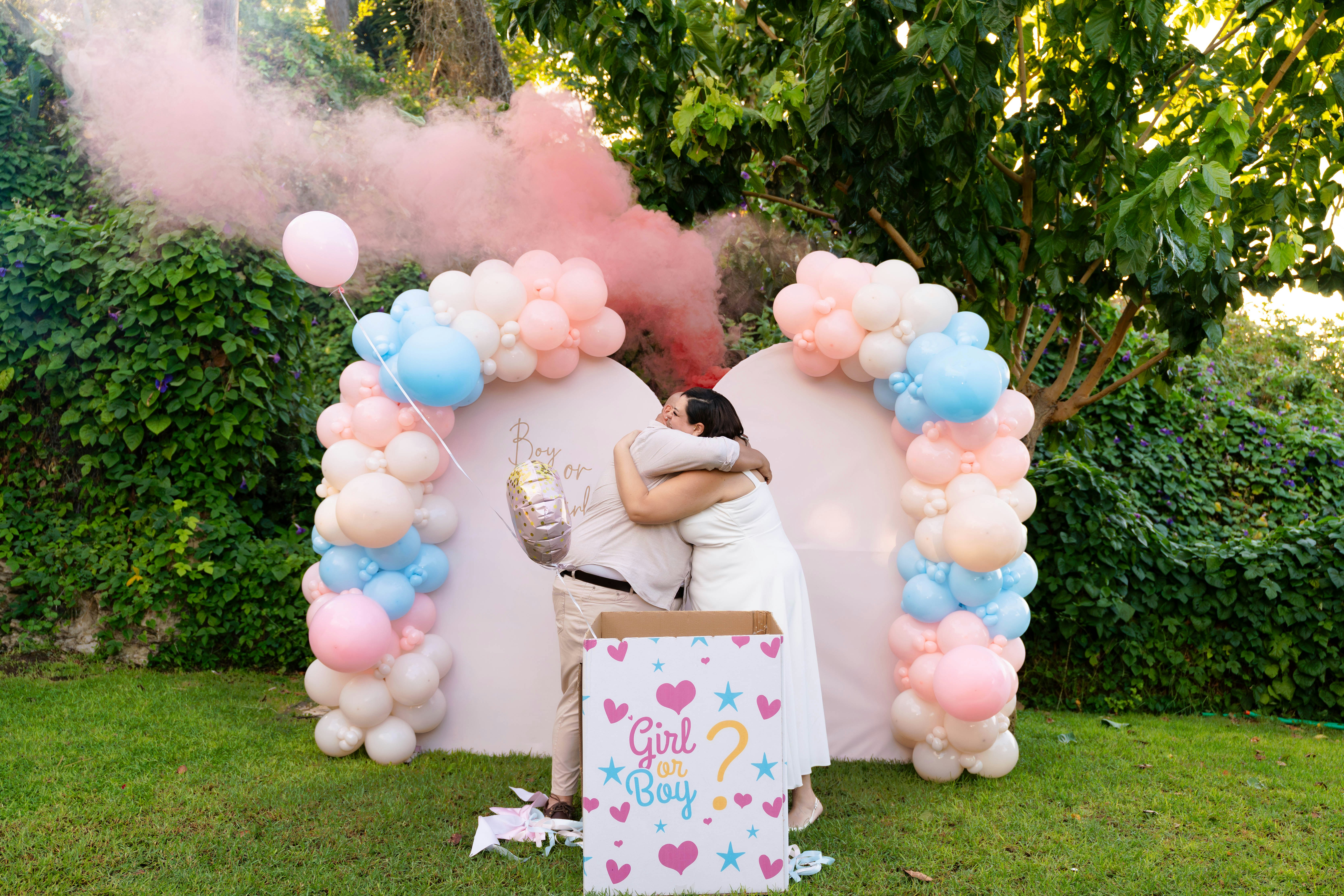 Soft-pink celebration arch framed by pastel balloons and a tender embrace
