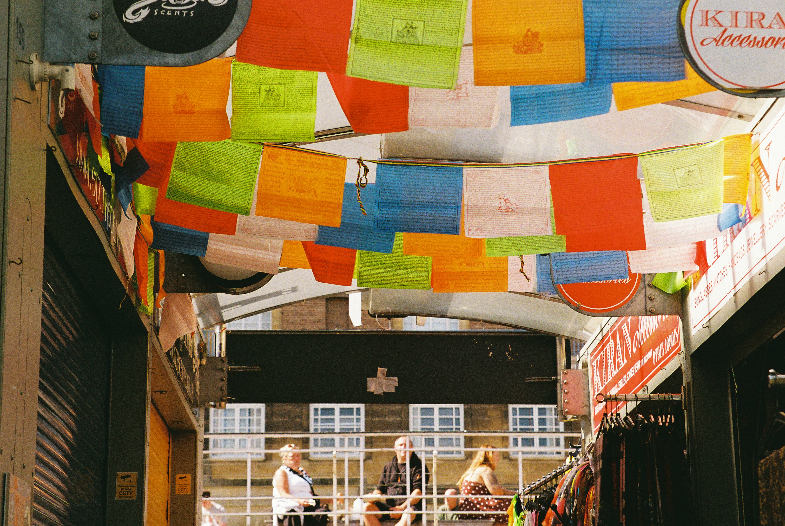 Colorful Shrine: Torn Flags and Market Cabins Framed by Sunlit Alley
